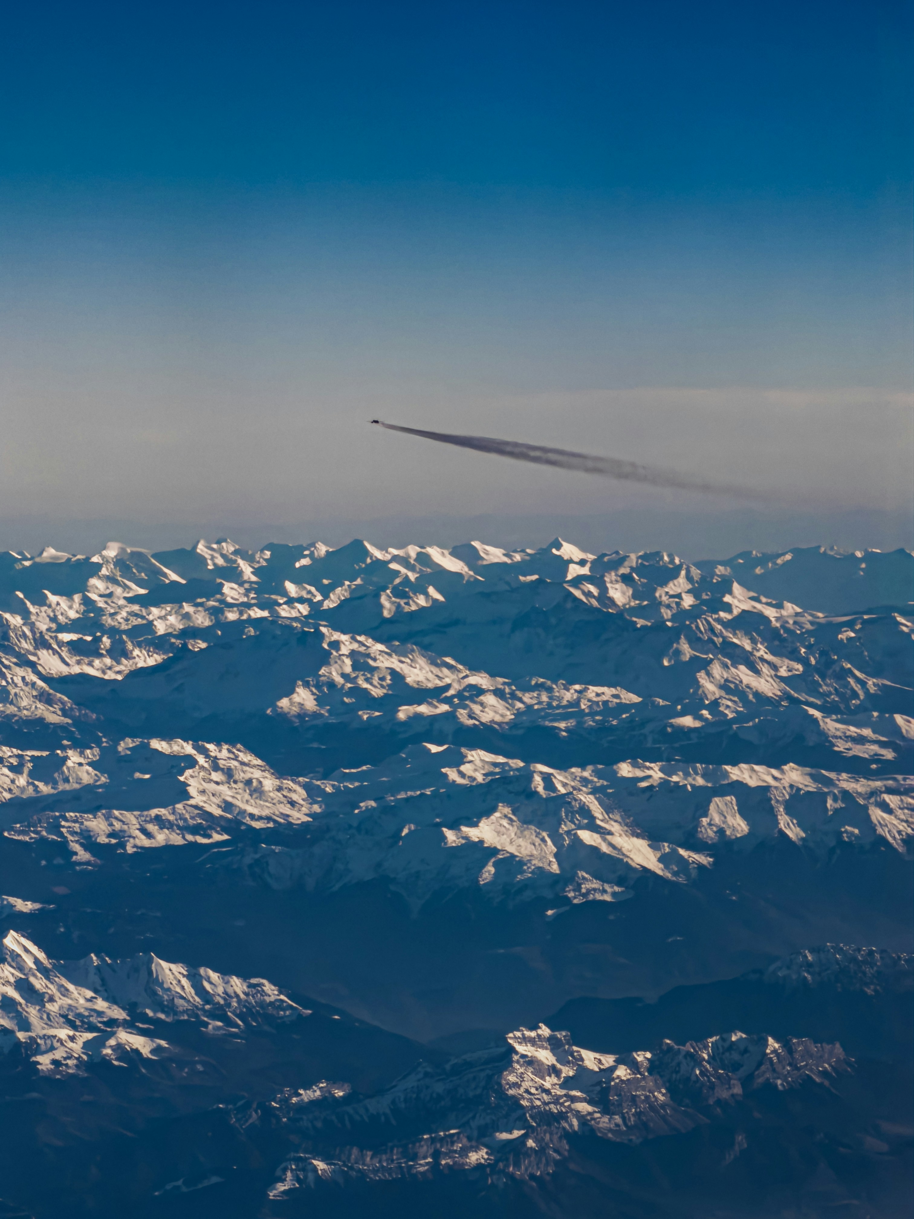 Aerial Wedge: Snow-Capped Peaks under a Jet Swoop