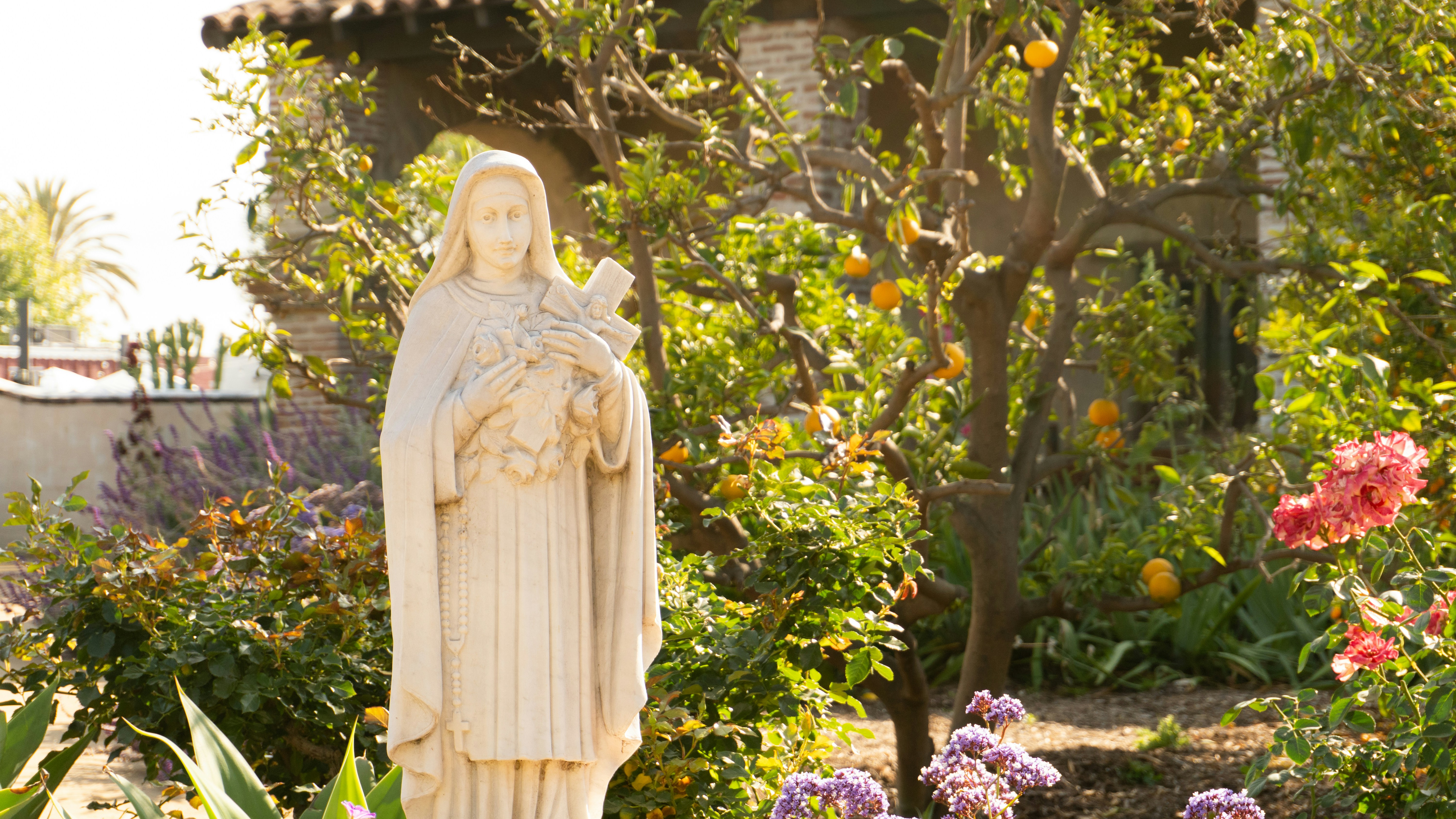 Statue of a hooded figure cradling a lion under a flowering garden canopy