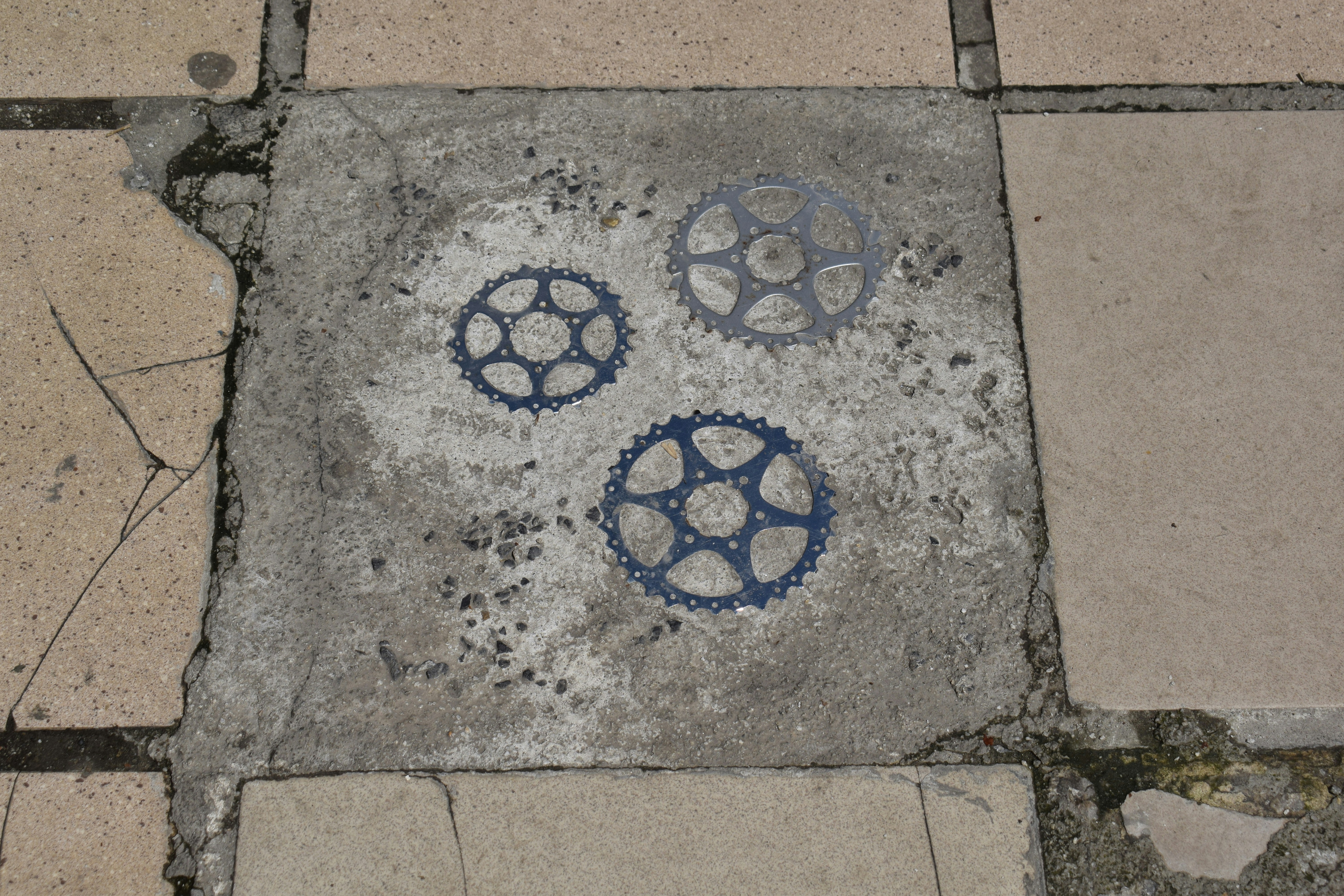 Three industrial nodes: worn manhole covers bloom on a concrete grid