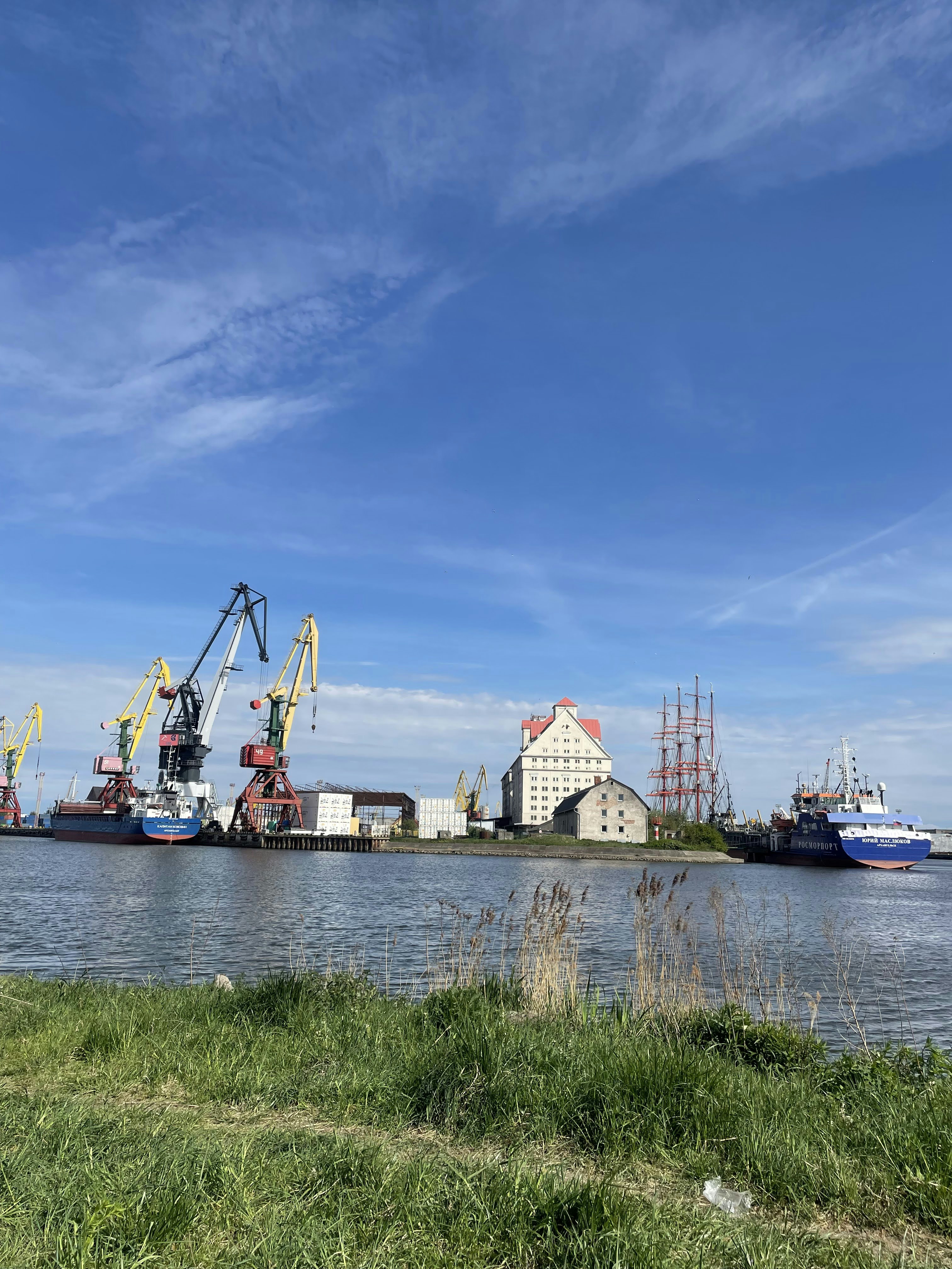 Industrial harbor at noon: cranes, ships, and a red-roofed warehouse