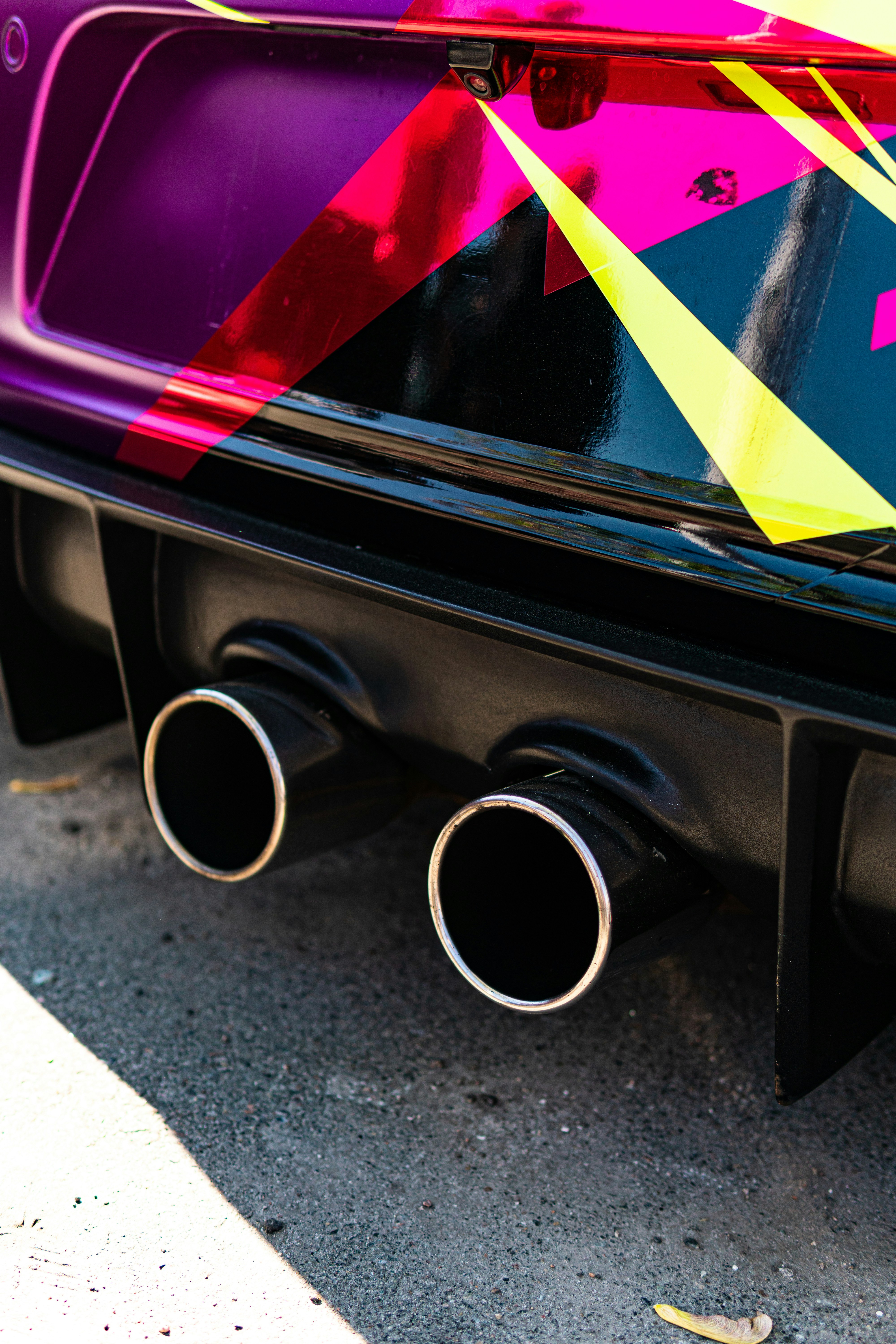 Vivid Geometric Fade: Dual Exhausts at the Back of a Neon-Tinted Car