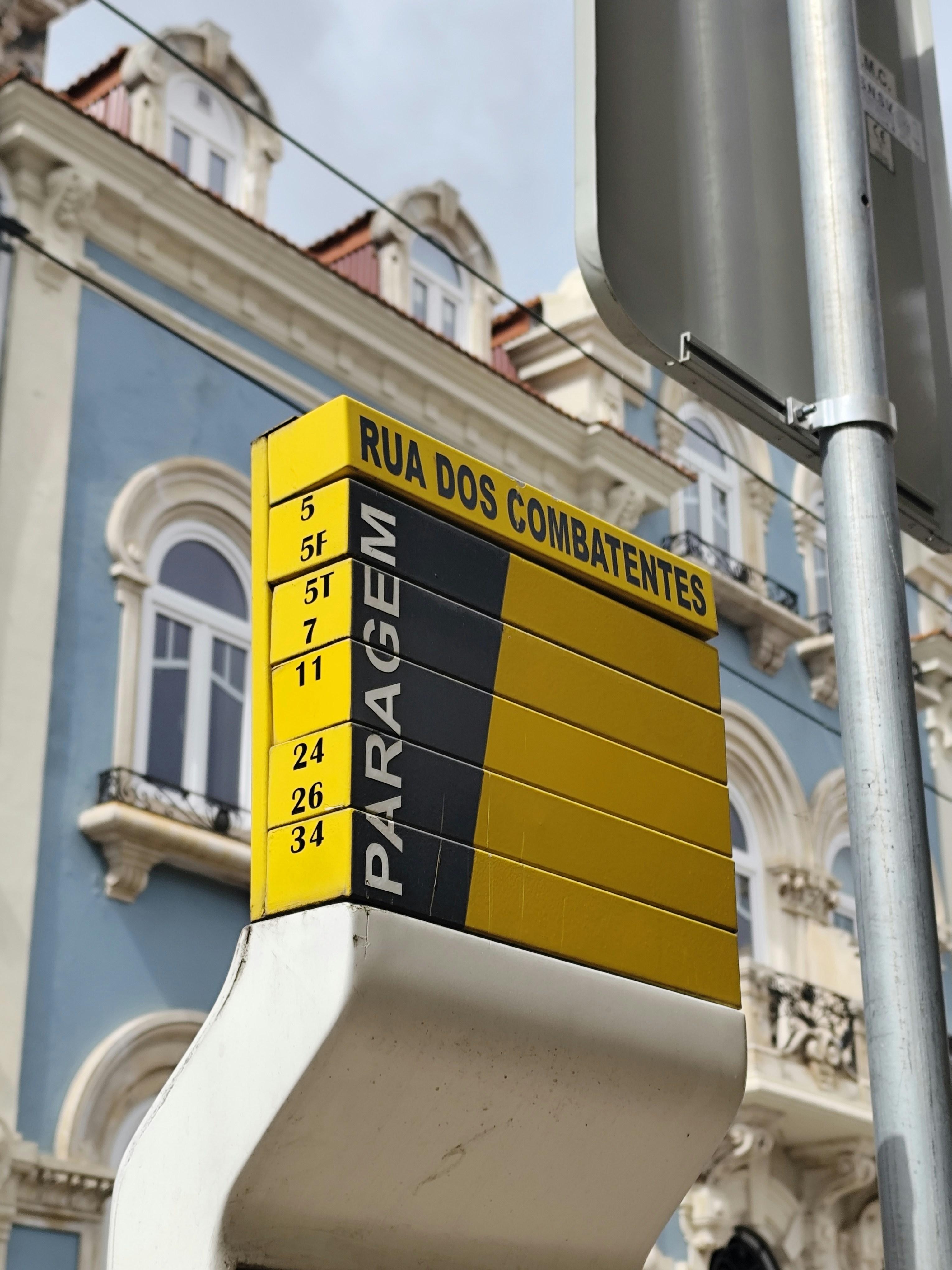 Signpost in Sunshine: A Street Marker Gaining Height Against a Blue Facade