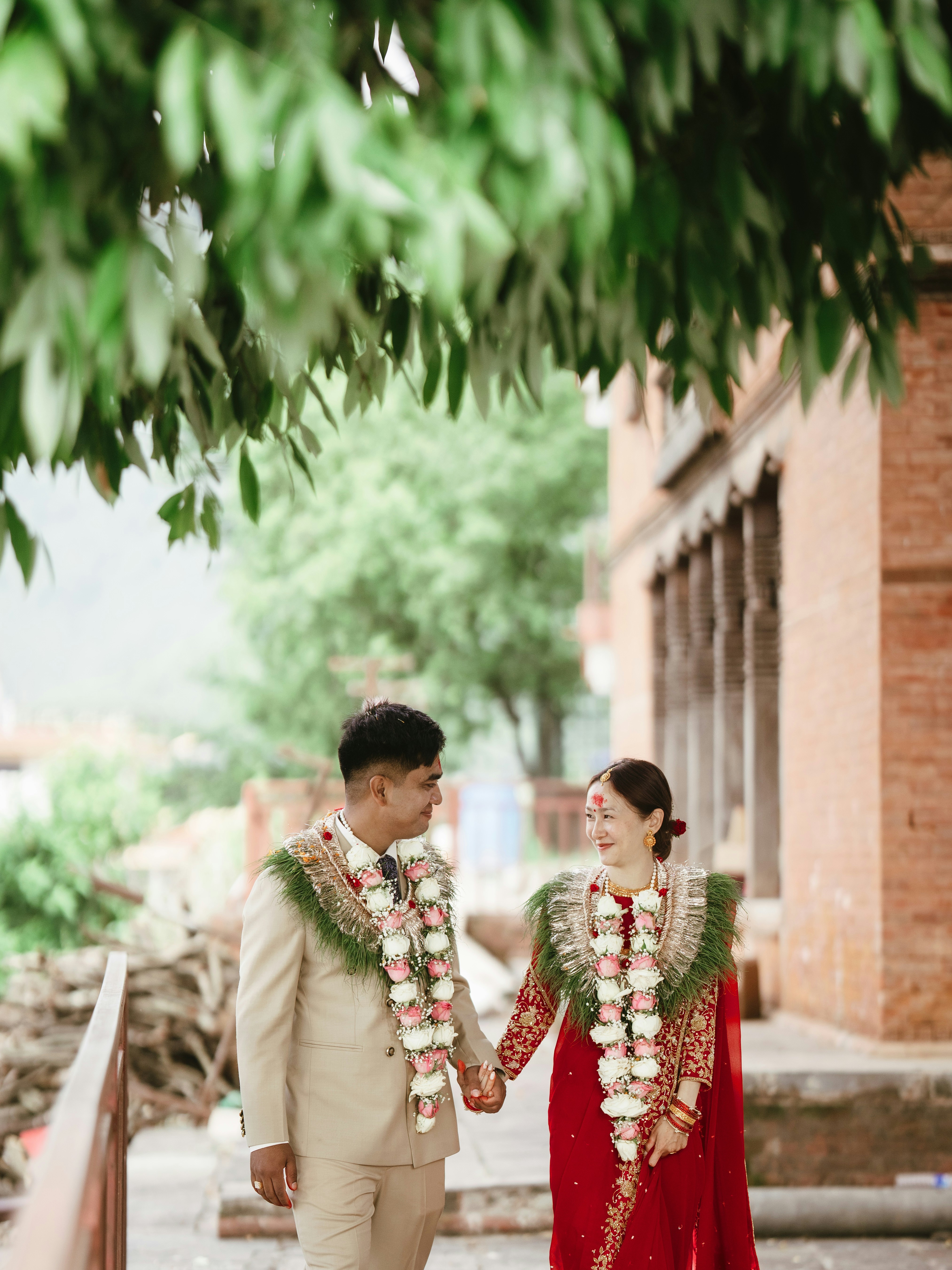 Bride and Groom in Garlands Walk Hand in Hand Under Greenery