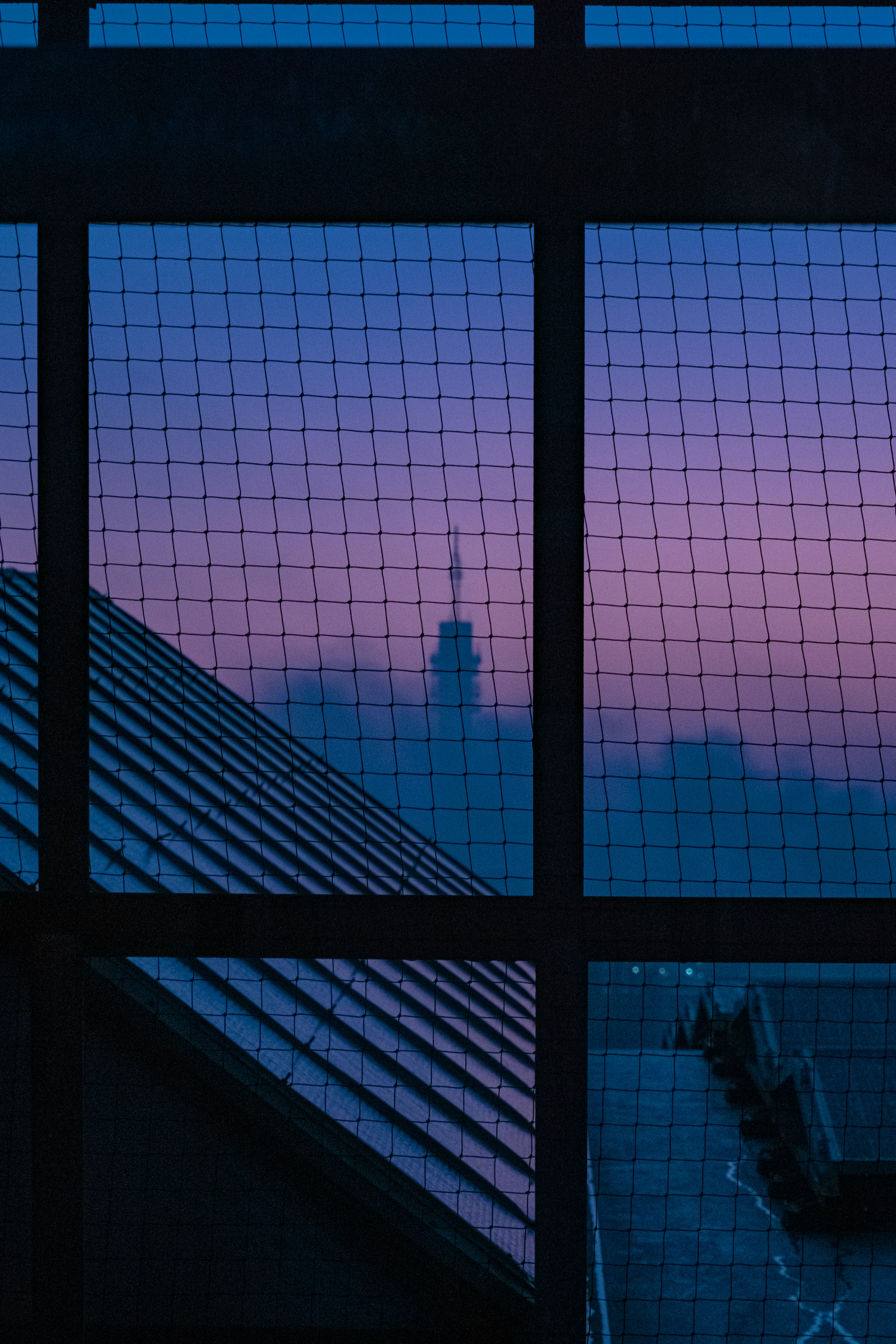 Grid of dusk: city silhouette through wire mesh and lattice