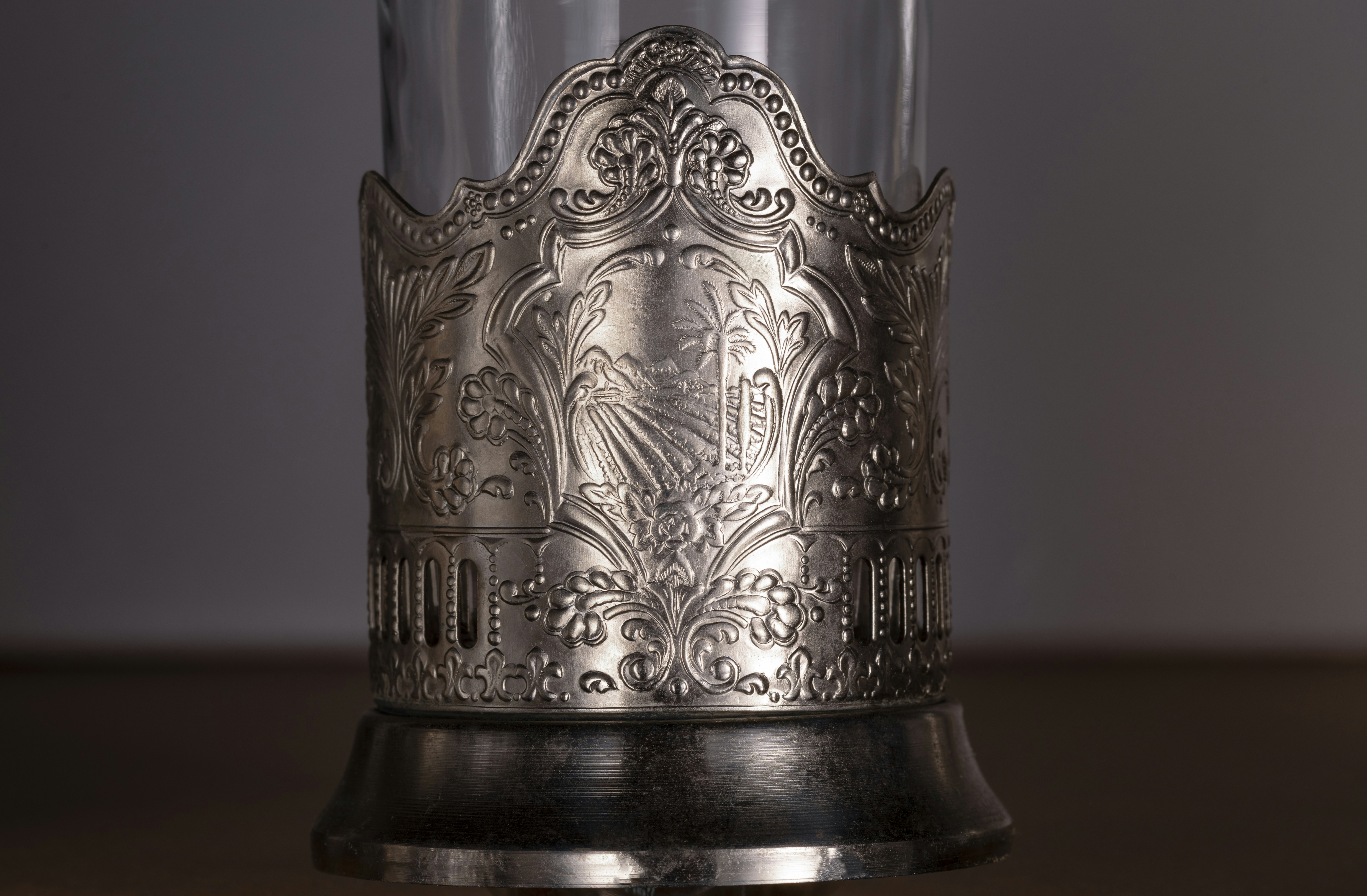 Close-up of an intricately engraved metal base with floral and scroll patterns on a dark, reflective surface.