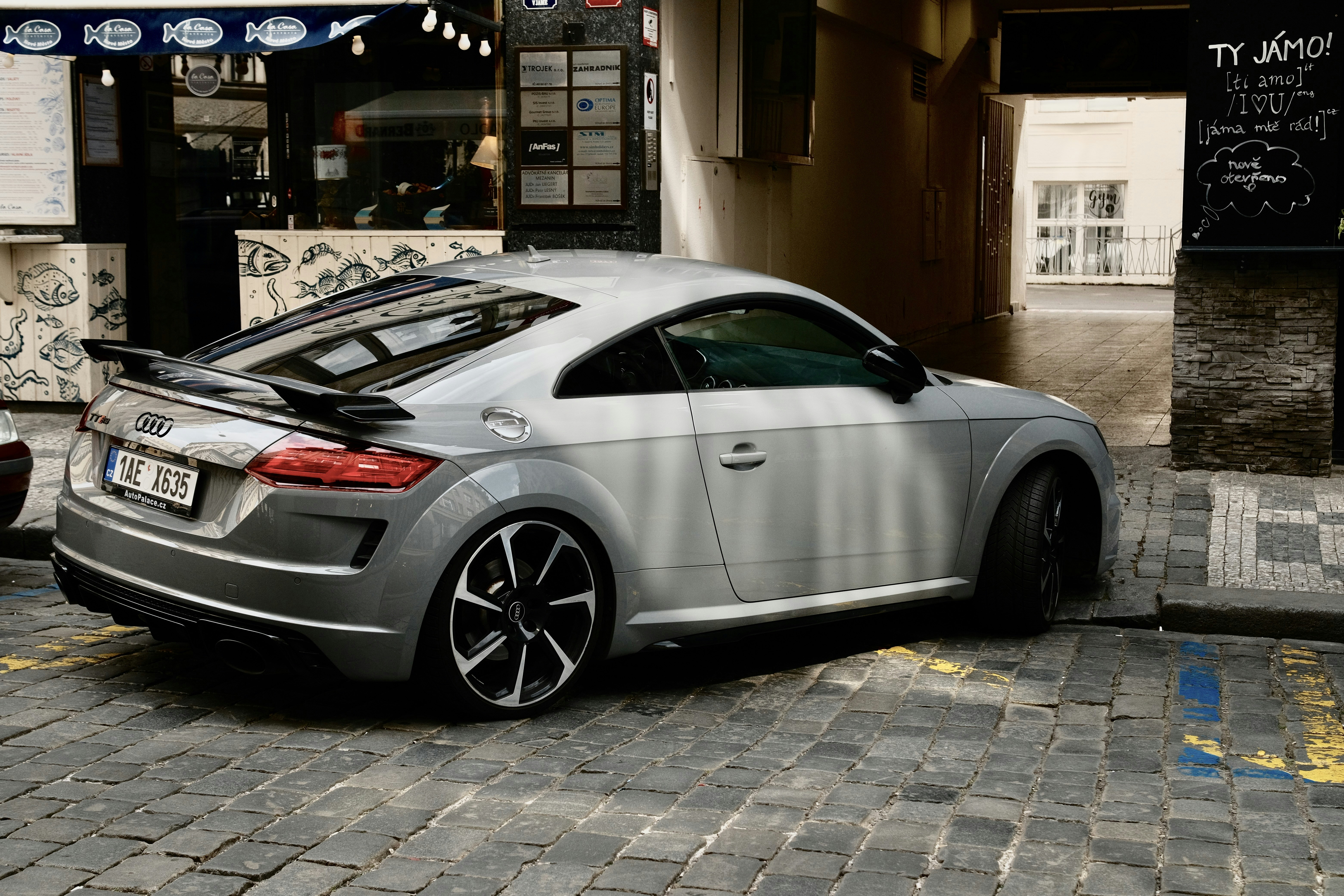 Sleek silver Audi parked on cobblestones outside a café