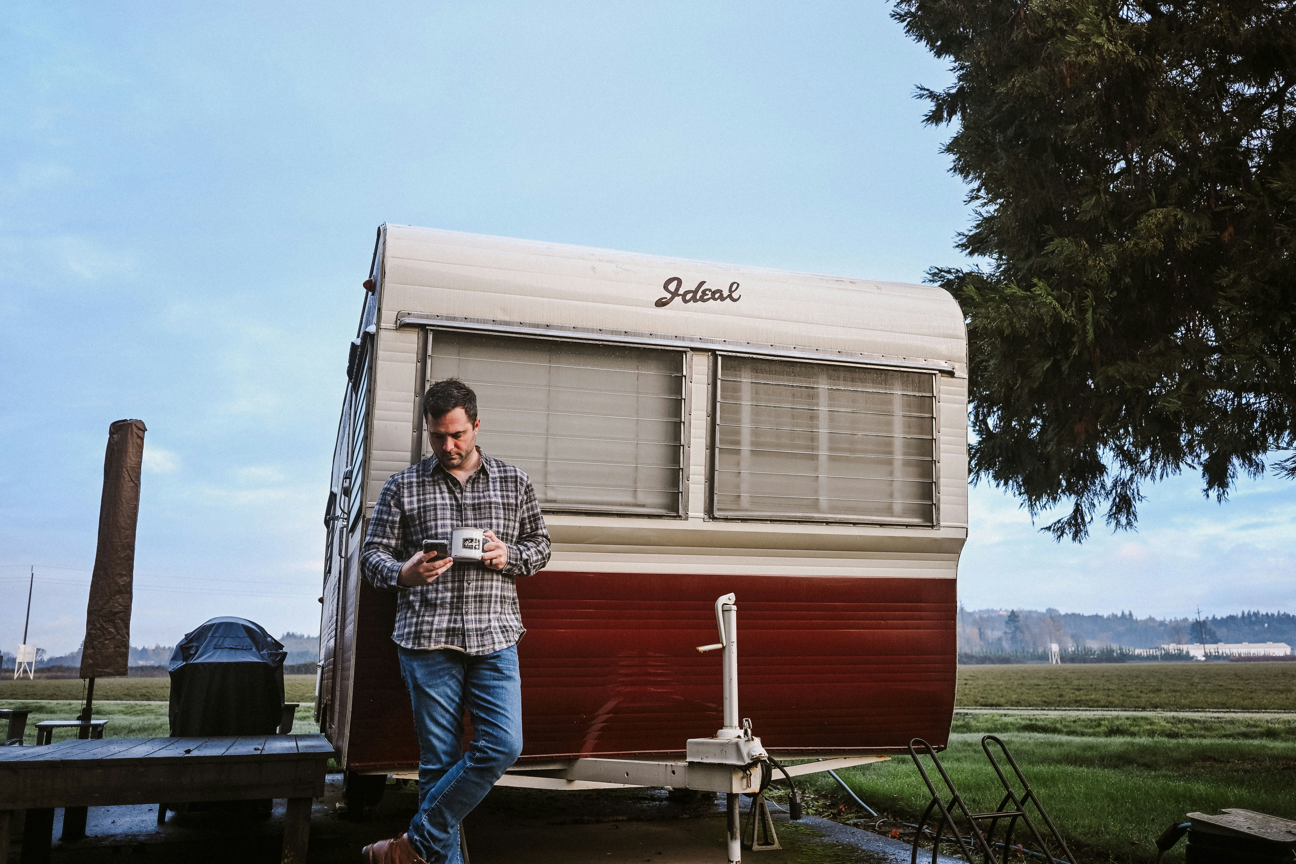Man standing by vintage travel trailer holding a cup.