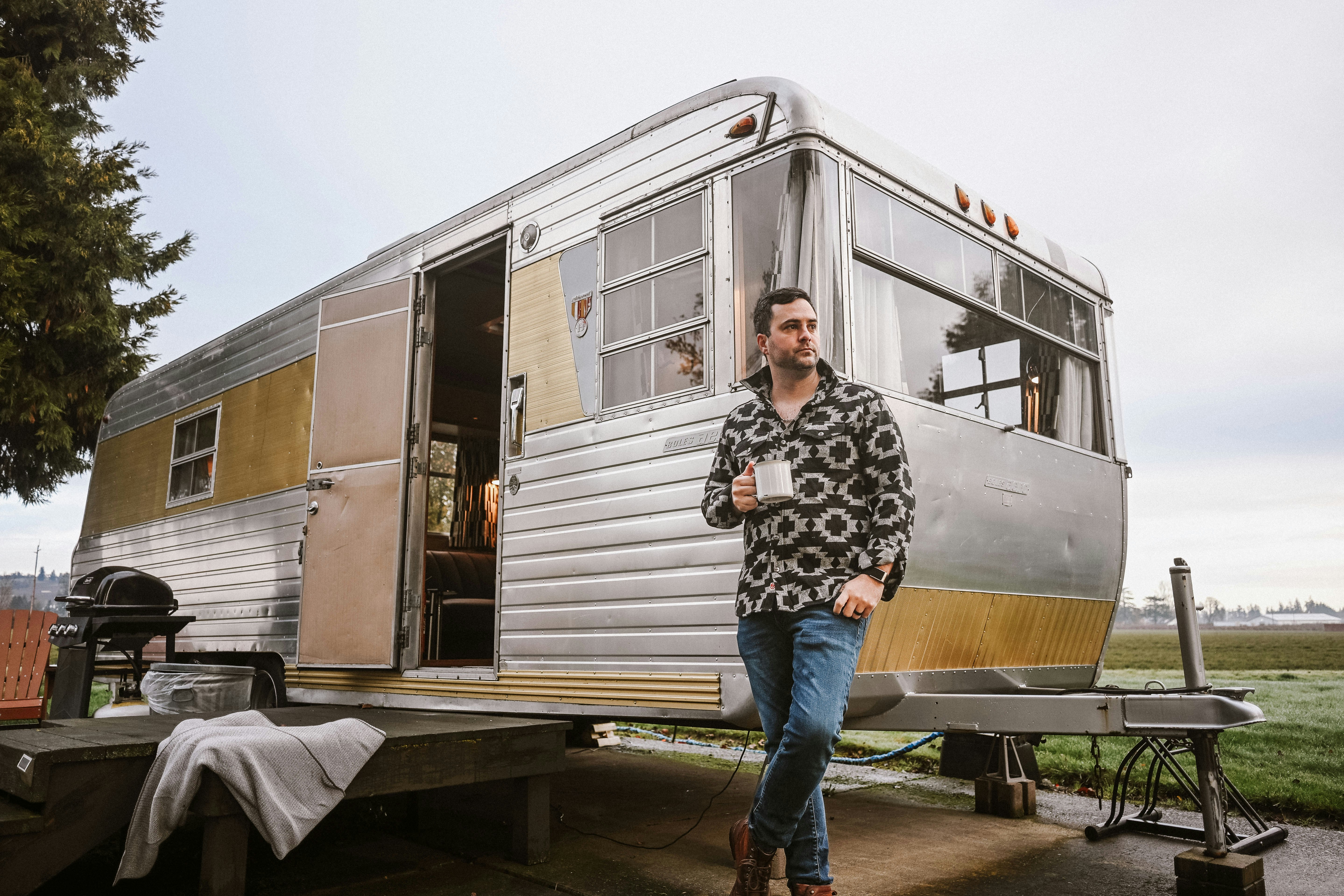 Man with mug on a vintage trailer under open sky