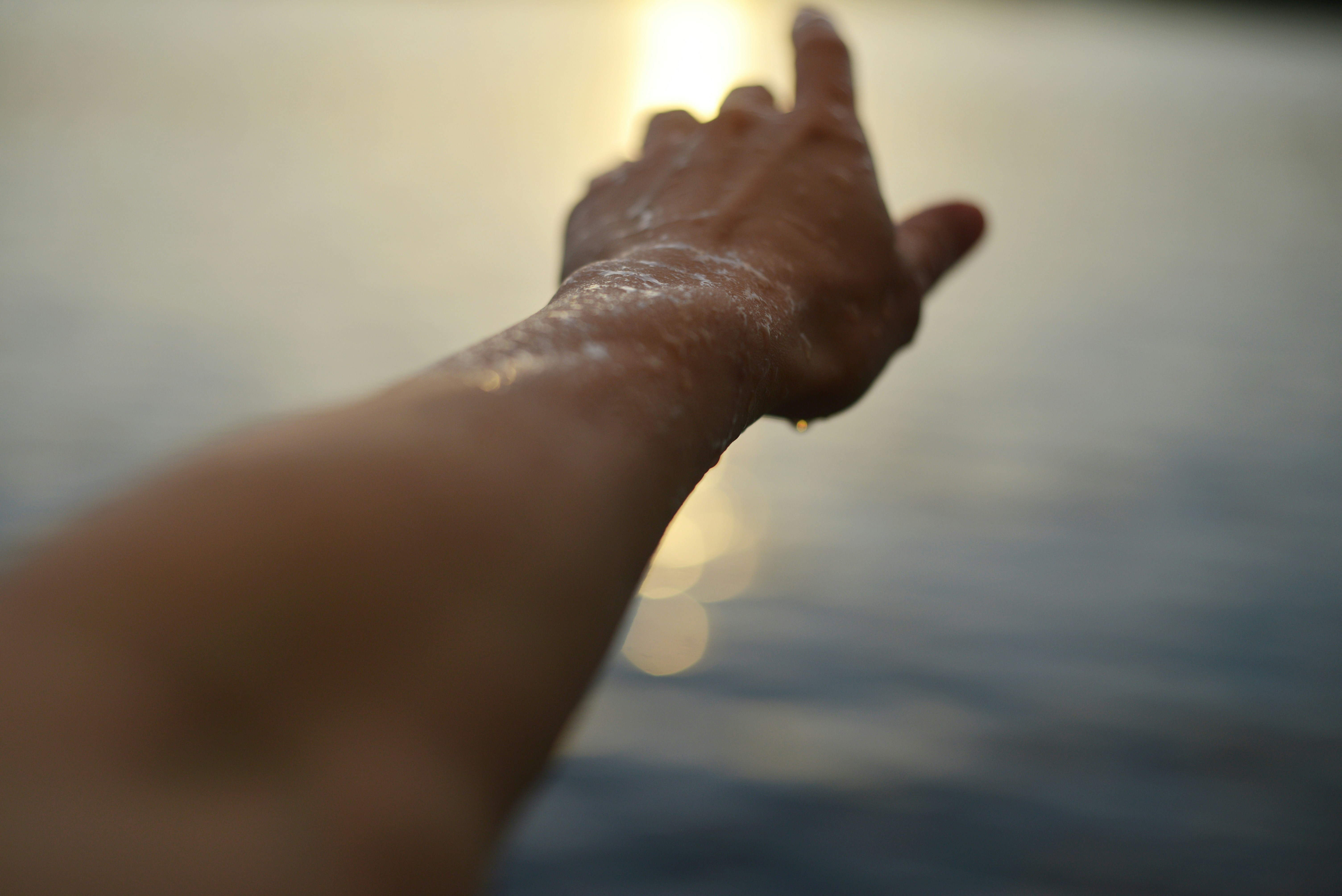 Reach for the Glimmer: A Close-Up Hand Against a Sunset Horizon