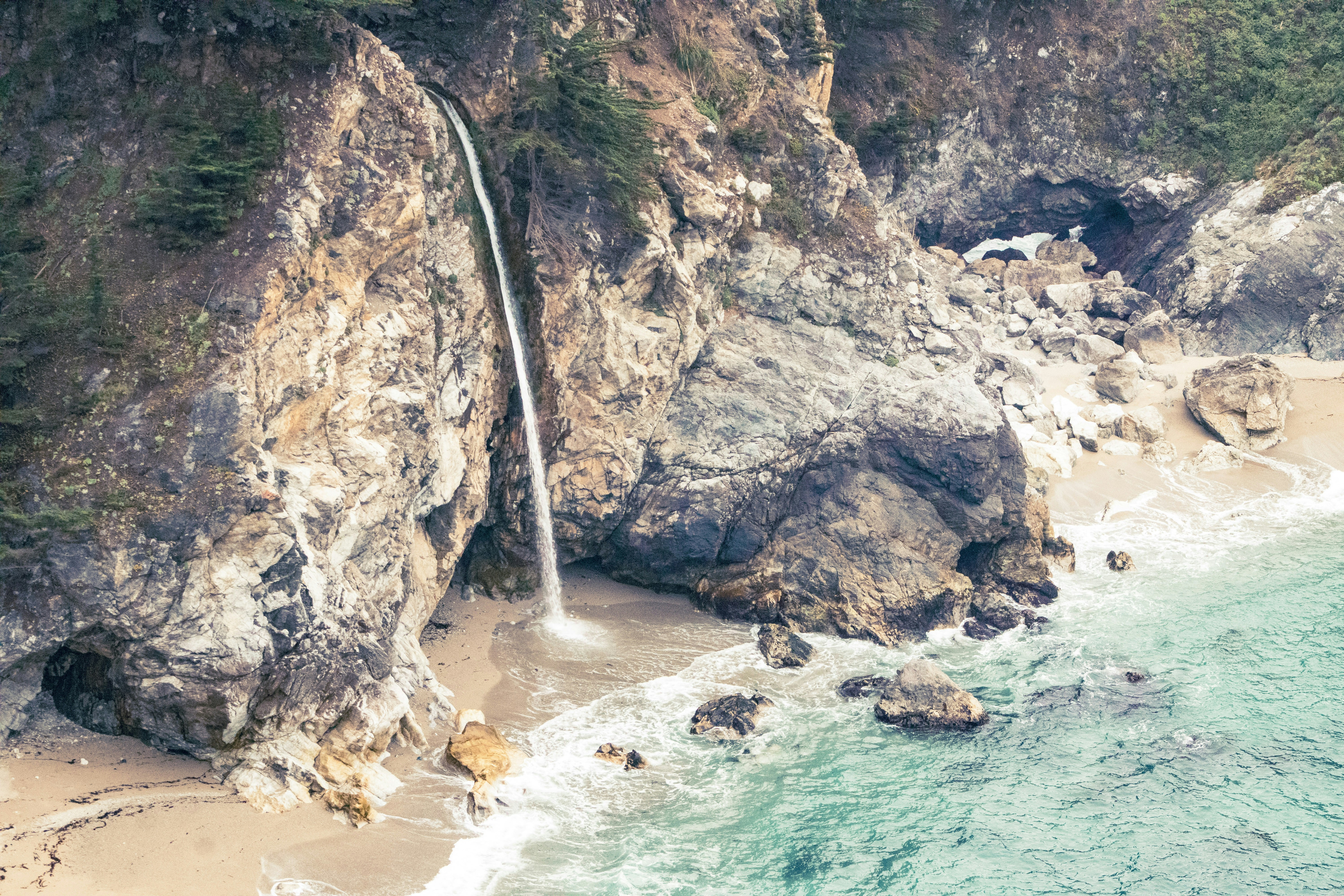 Coastal Curtain: A Narrow Waterfall Tumbles Over Cliff into Turquoise Cove
