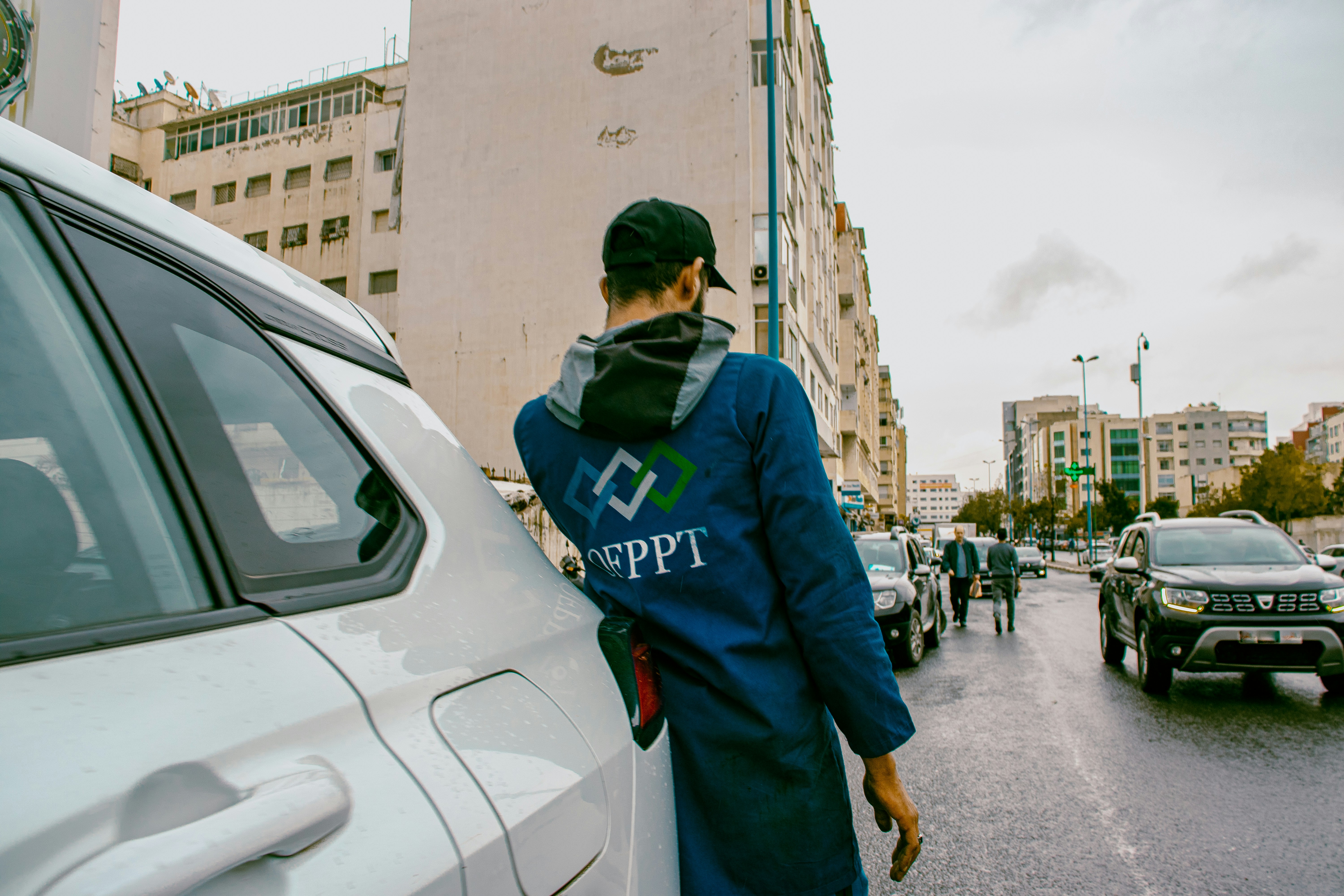 Urban Crossing: A Figure in a Blue Coat Steps Back from a City Car Line