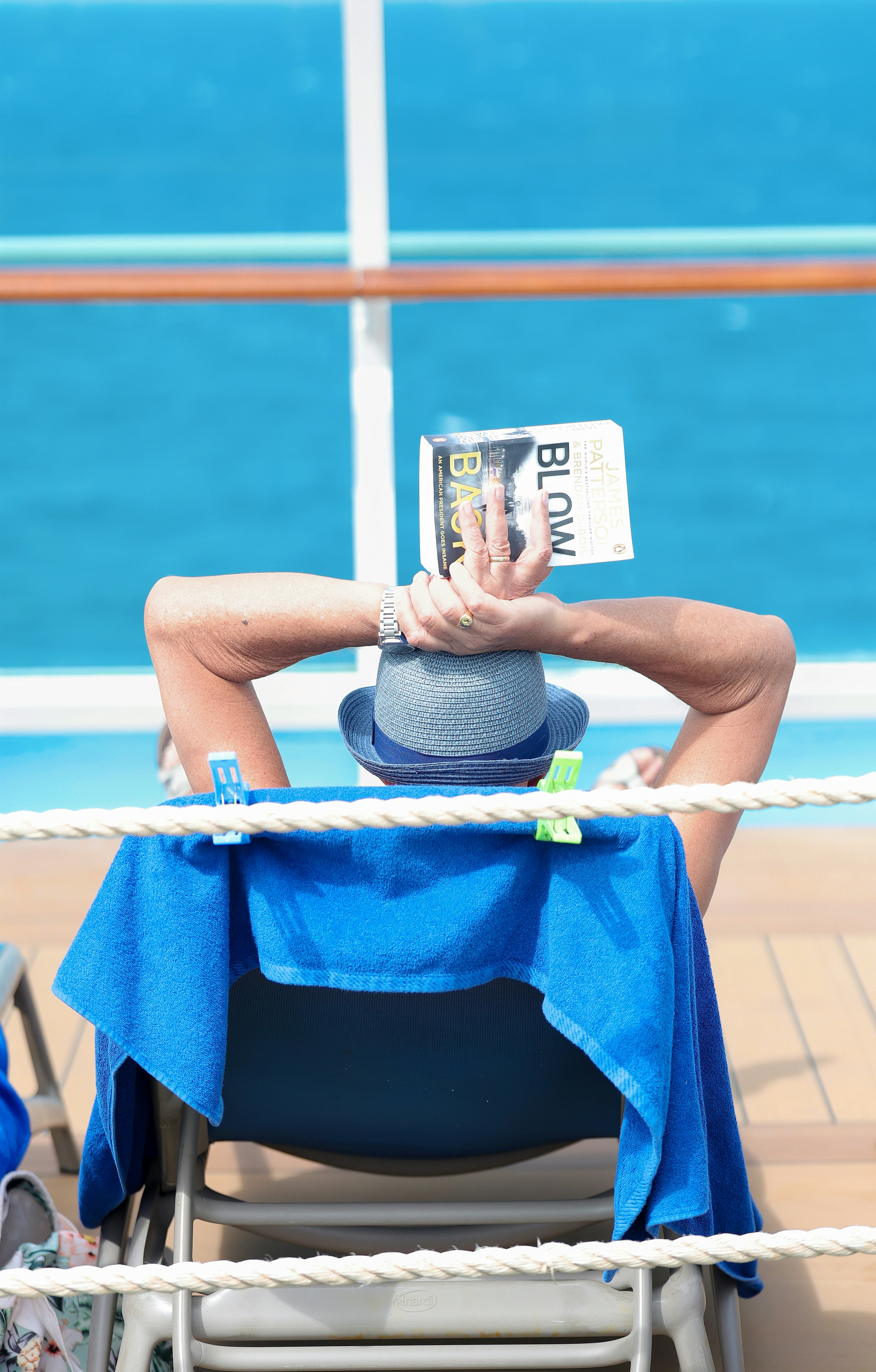 Person relaxing on a cruise deck, reading a book.