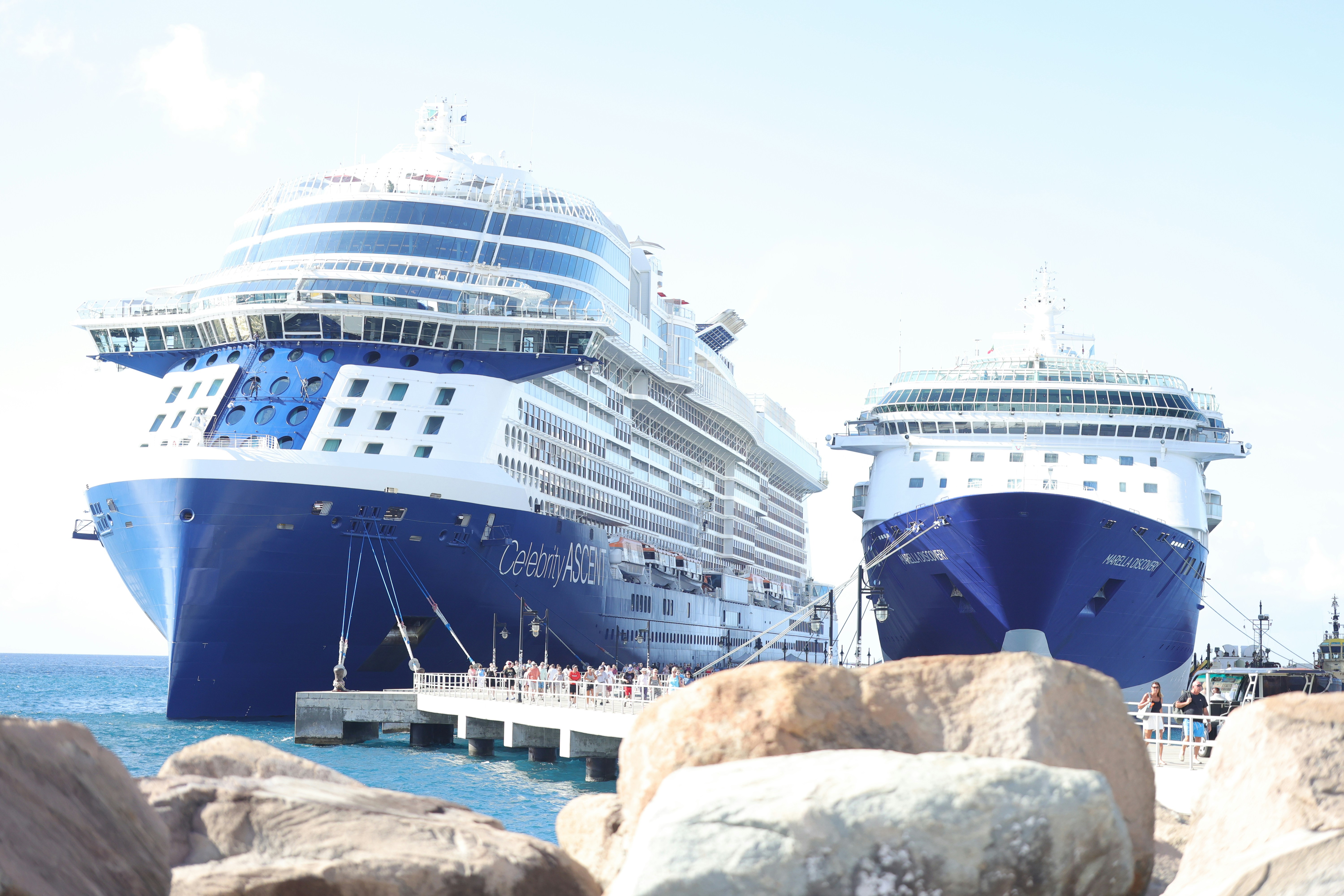 Two large cruise ships docked at a pier with people.
