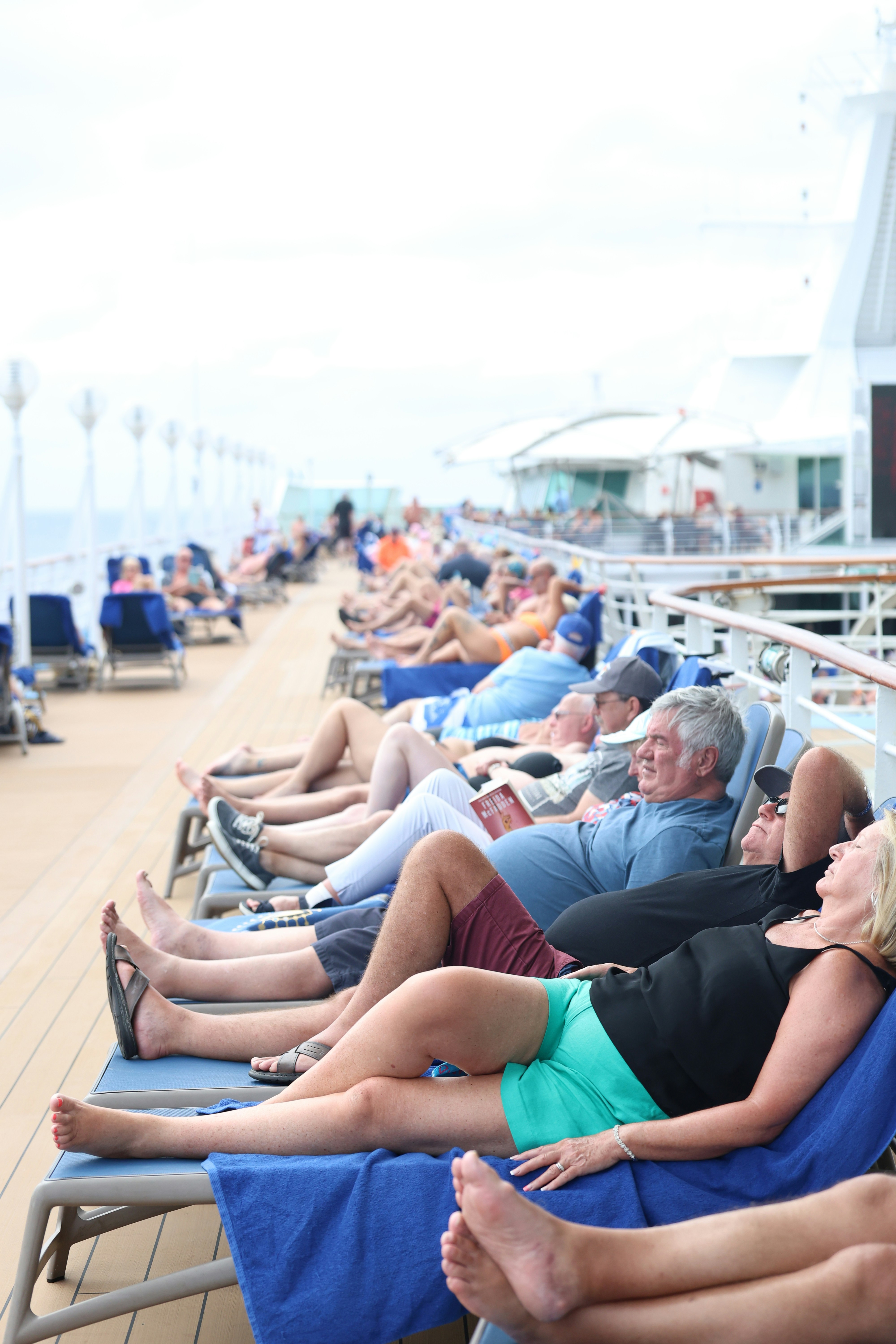 Sun-soaked loungers on a cruise deck, a crowd of vacationers basking along the railing