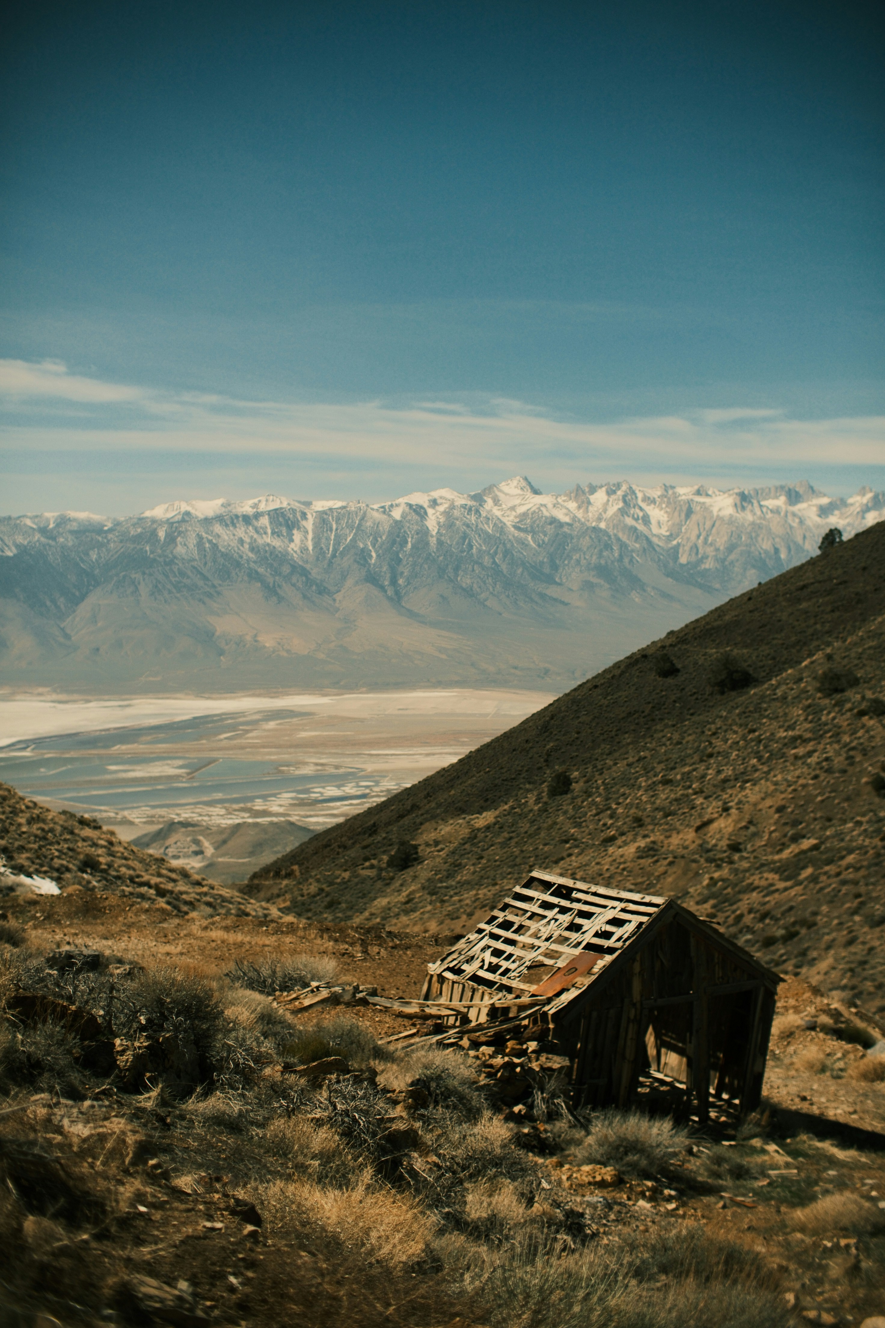 Sun-bleached hillside and abandoned shelter against a snow-capped panorama