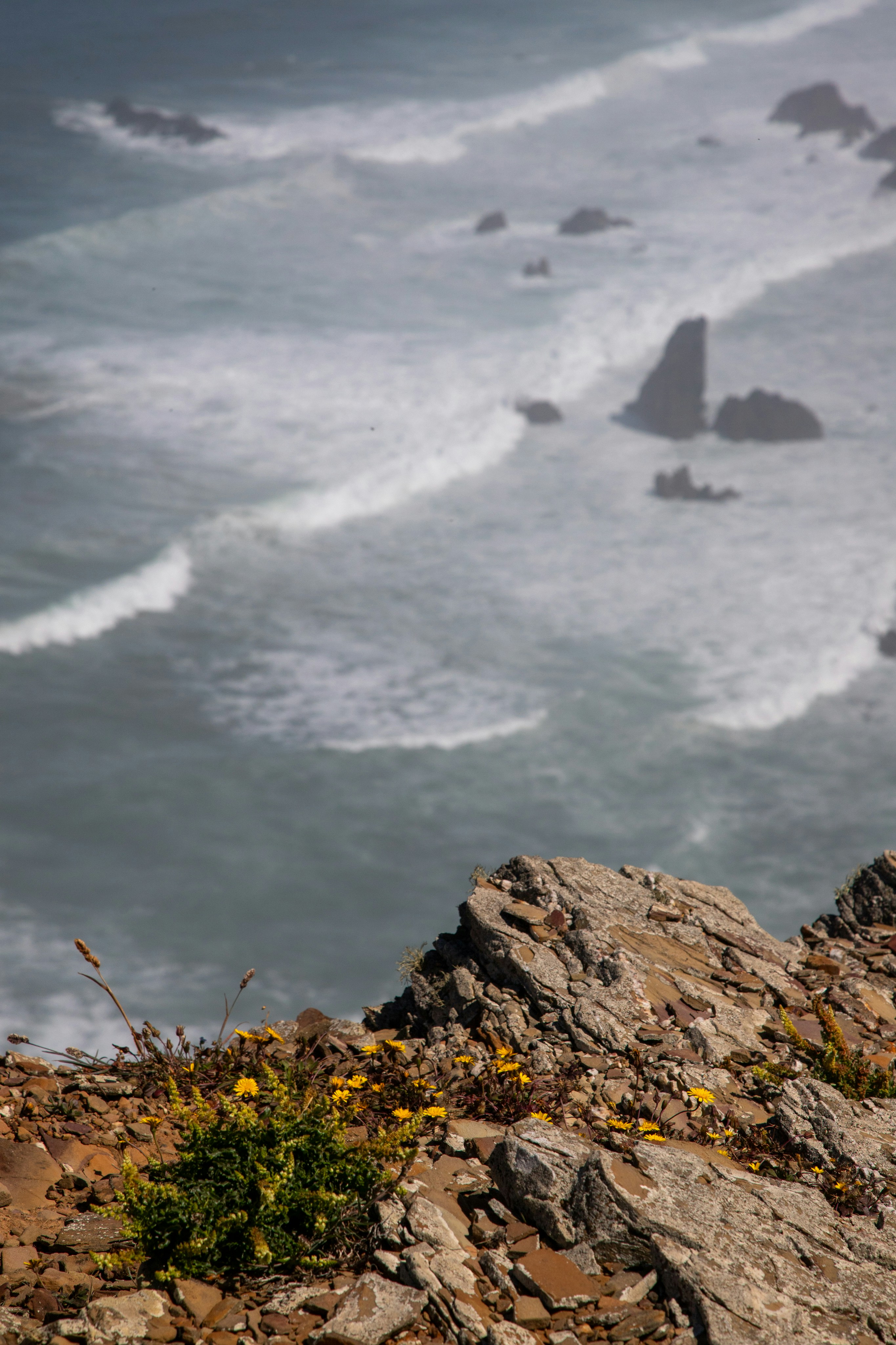 Rocky cliff overlooking a wavy ocean with distant rock formations.