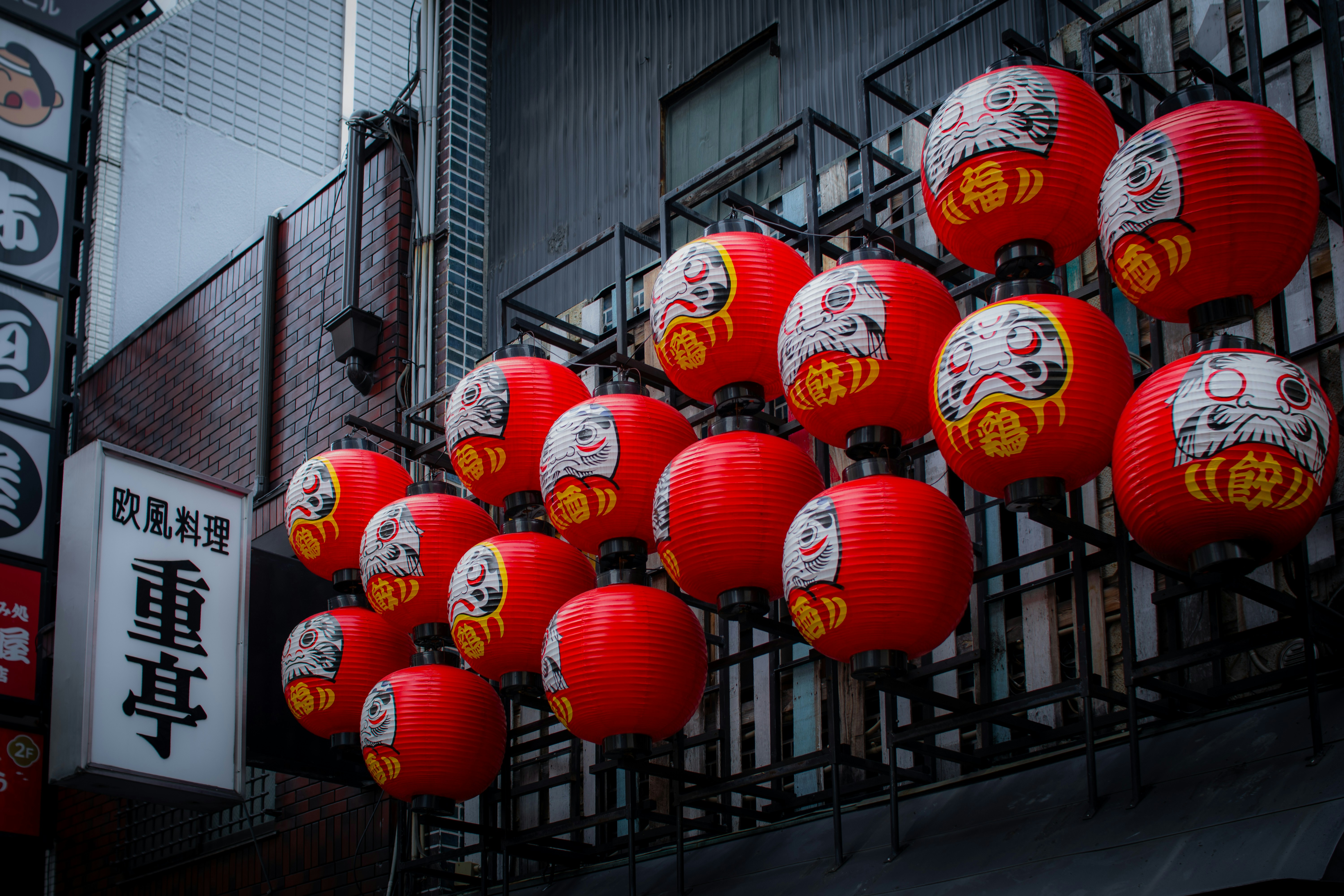 Cluster of red lanterns with decorative faces hangs against a dark storefront, emphasizing a traditional Asian street scene.