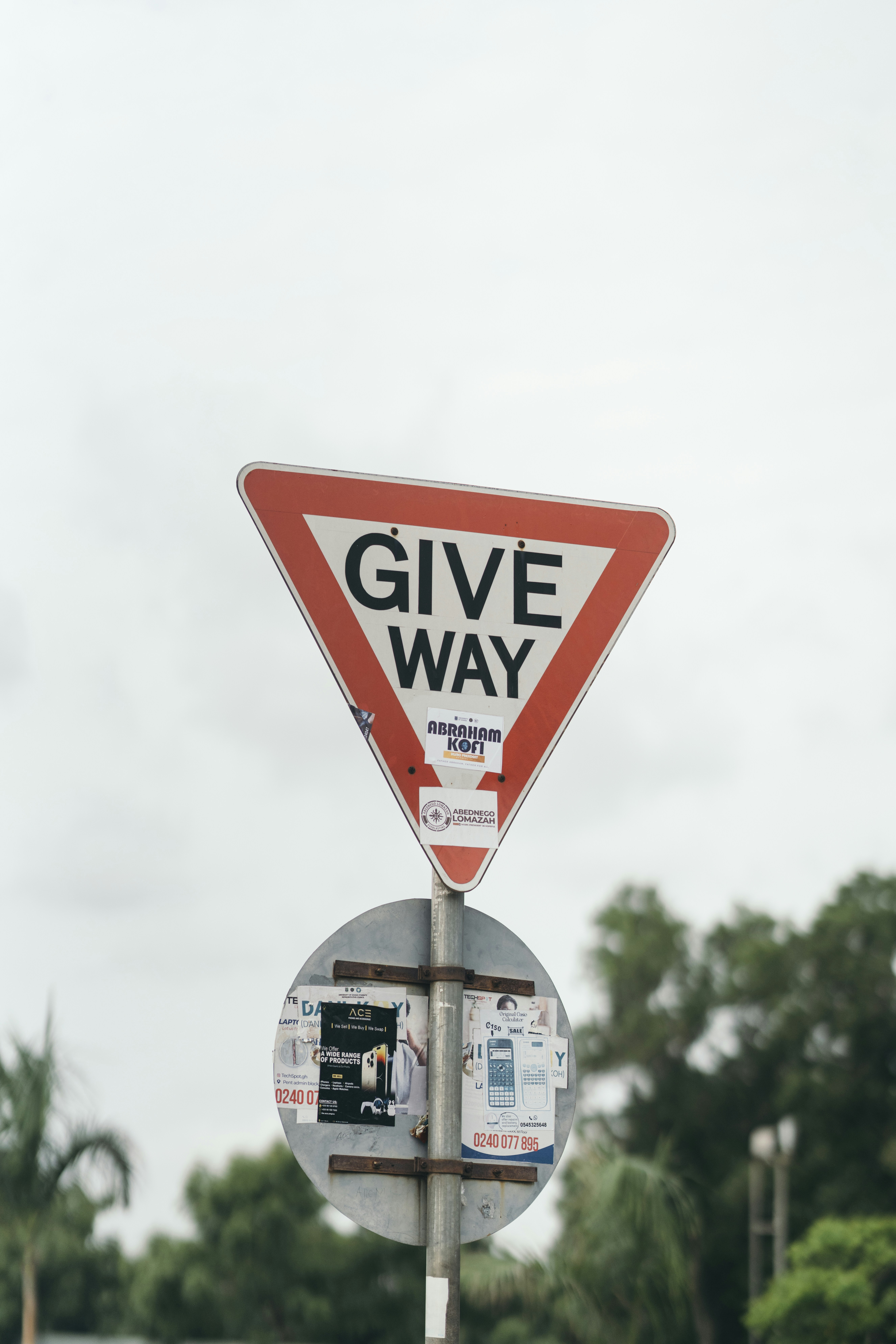 Give Way Sign: A Quiet Street Whispered Through a Poster-Pinned Obelisk