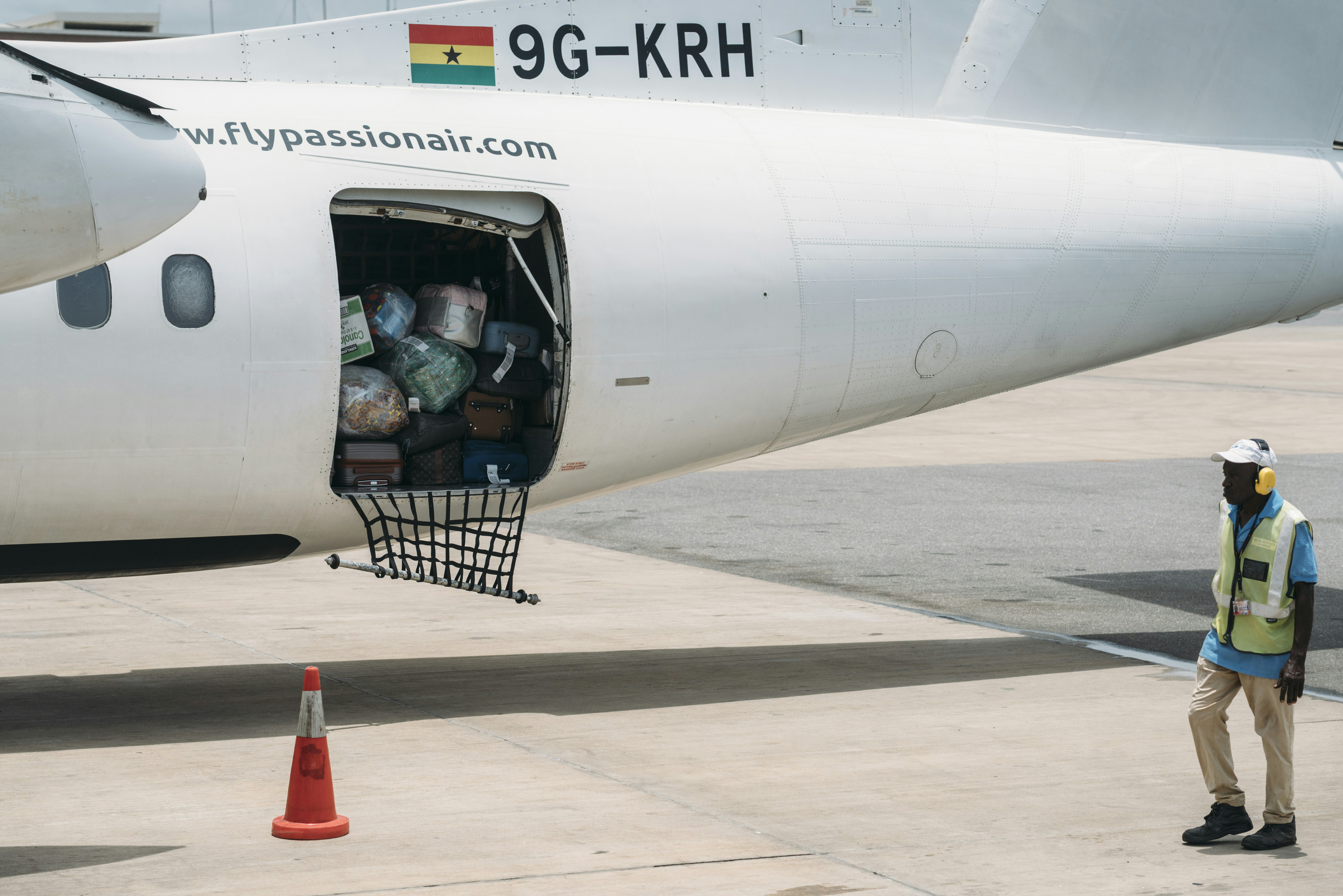 Cargo hold opened on a regional airliner as bags are loaded, with a ground crew member in a reflective vest nearby on the tarmac.