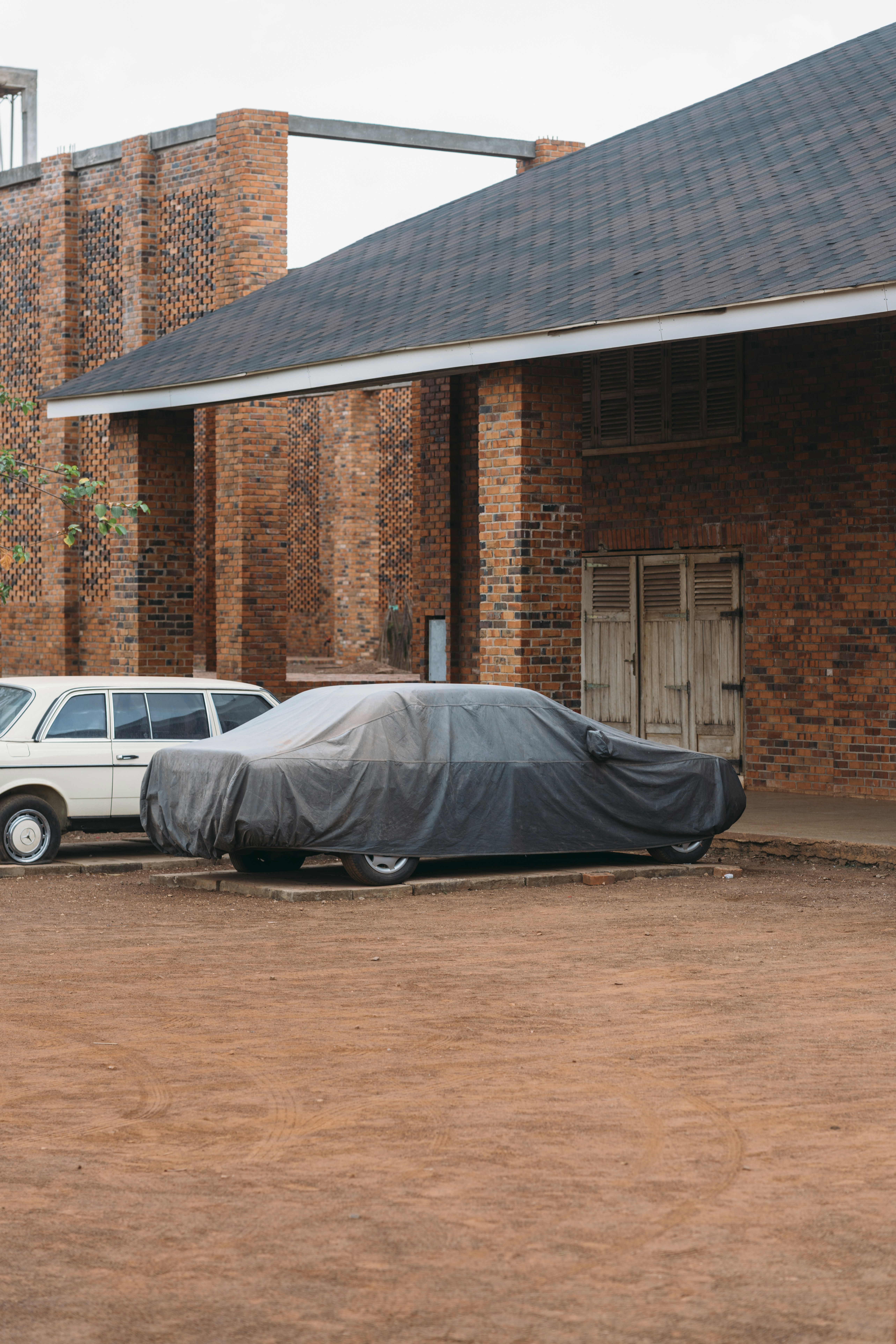 Hidden Car Under a Weathered Cover Near a Brick Garage
