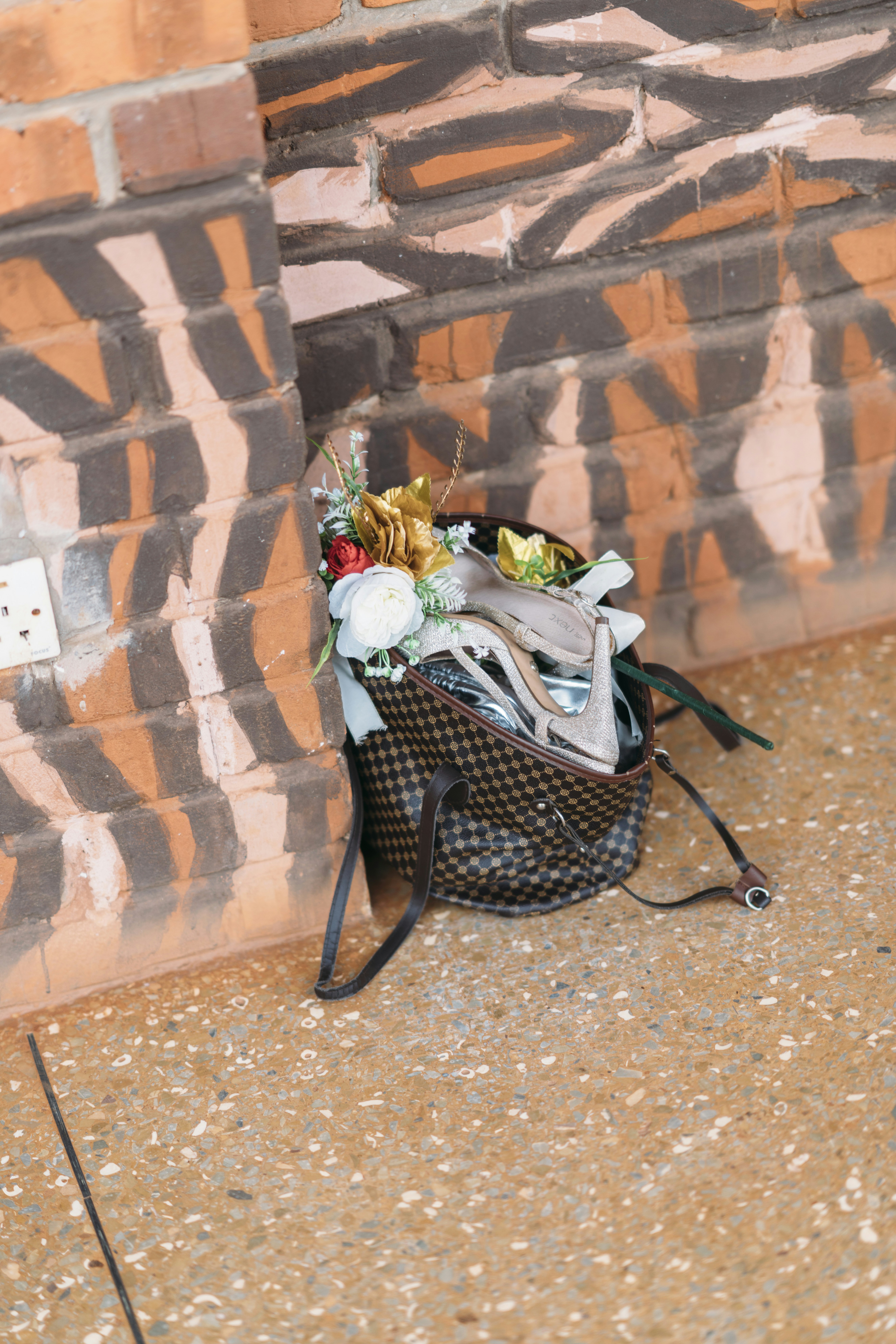 A stray bouquet rests inside a patterned handbag by a brick wall