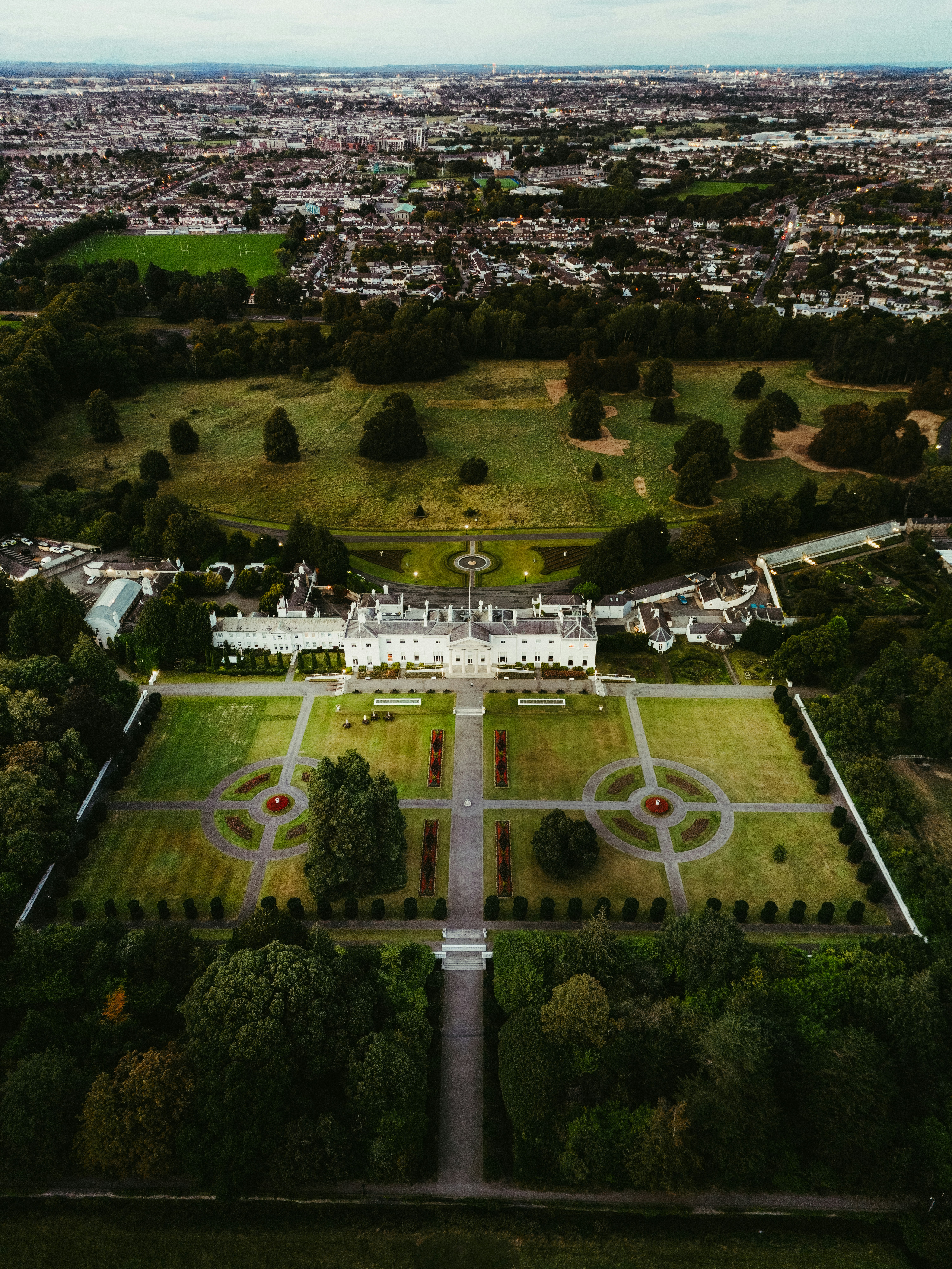 Elegant white mansion and formal gardens surrounded by urban landscape.