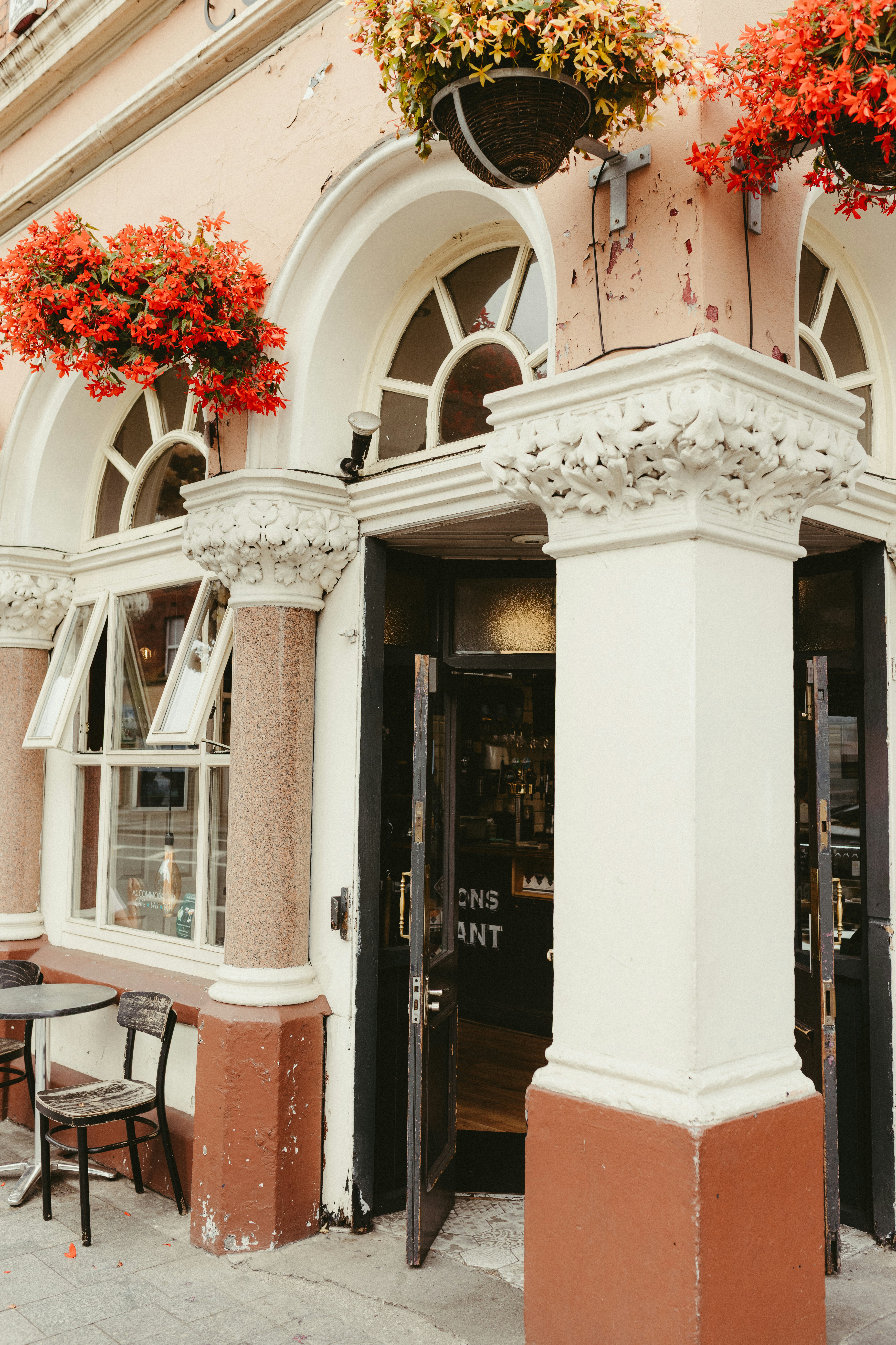 Facade of a vintage café: white arches, red flowers, and open doors