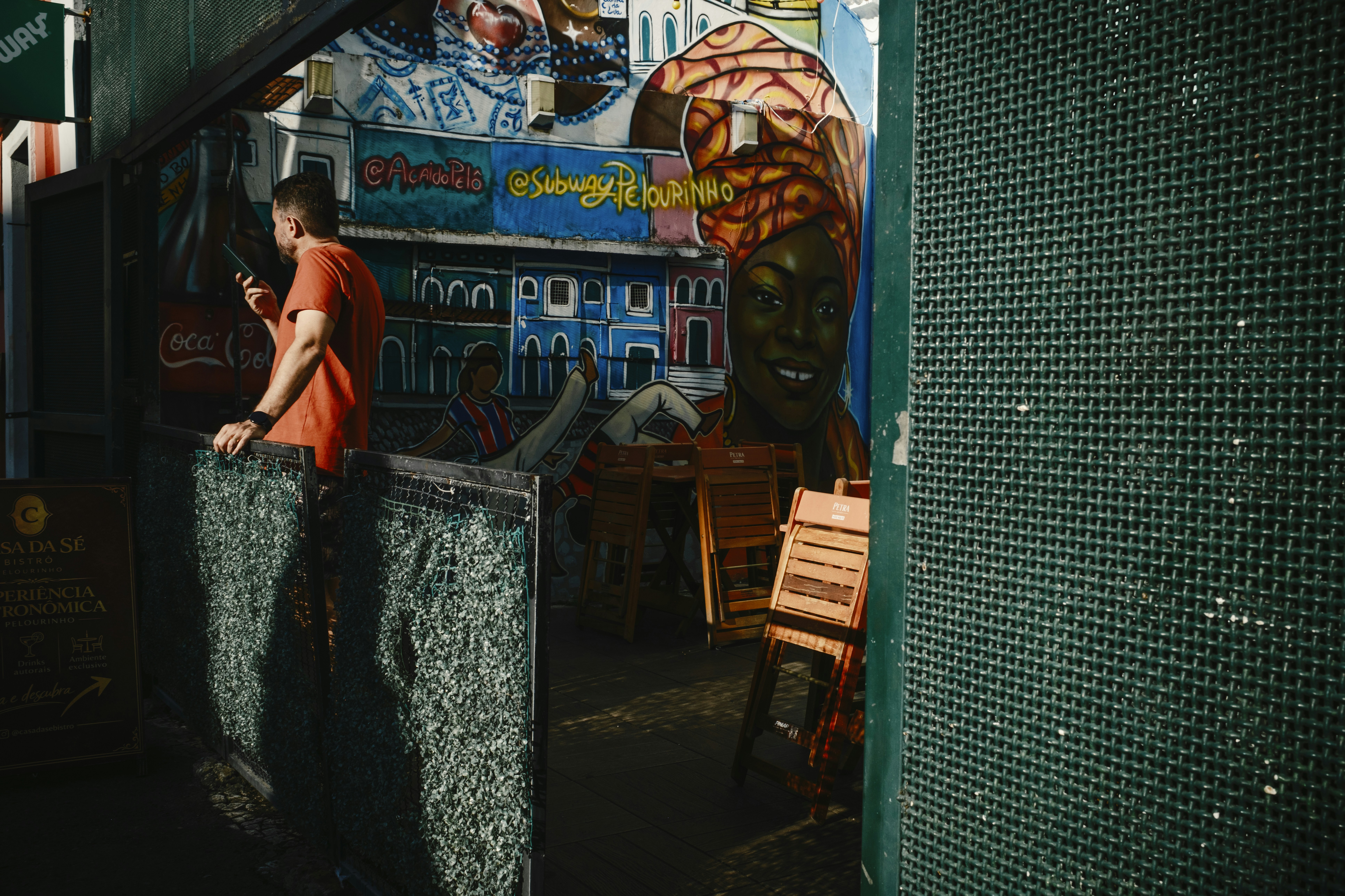 Sunlit Street Portrait Amid Colorful Murals and Green Fencing