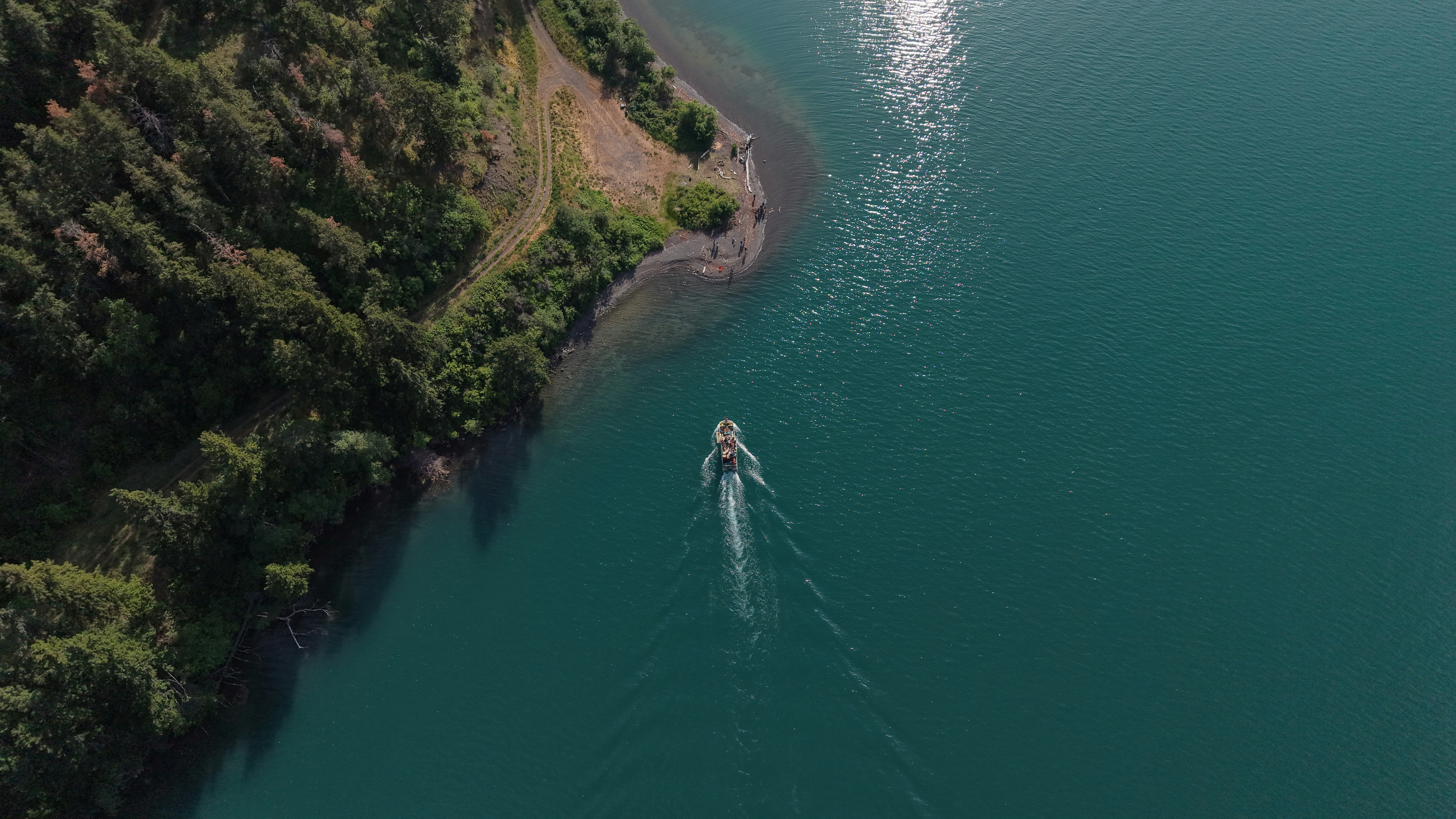 Isolated Wake: A lone boater carves a silver trail along emerald shoreline