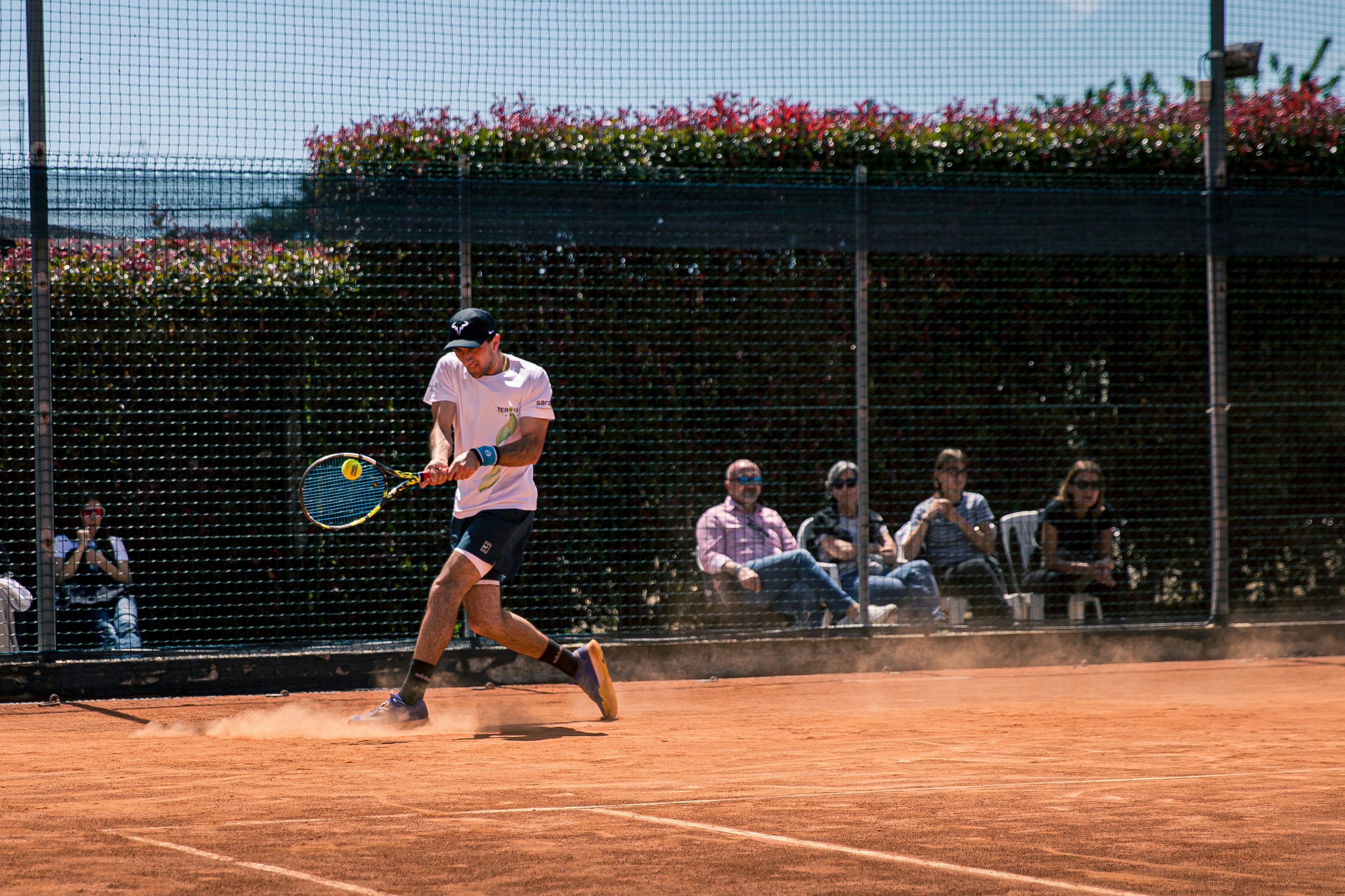 Tennis swing on clay: a serve under the sun with spectators in the backdrop