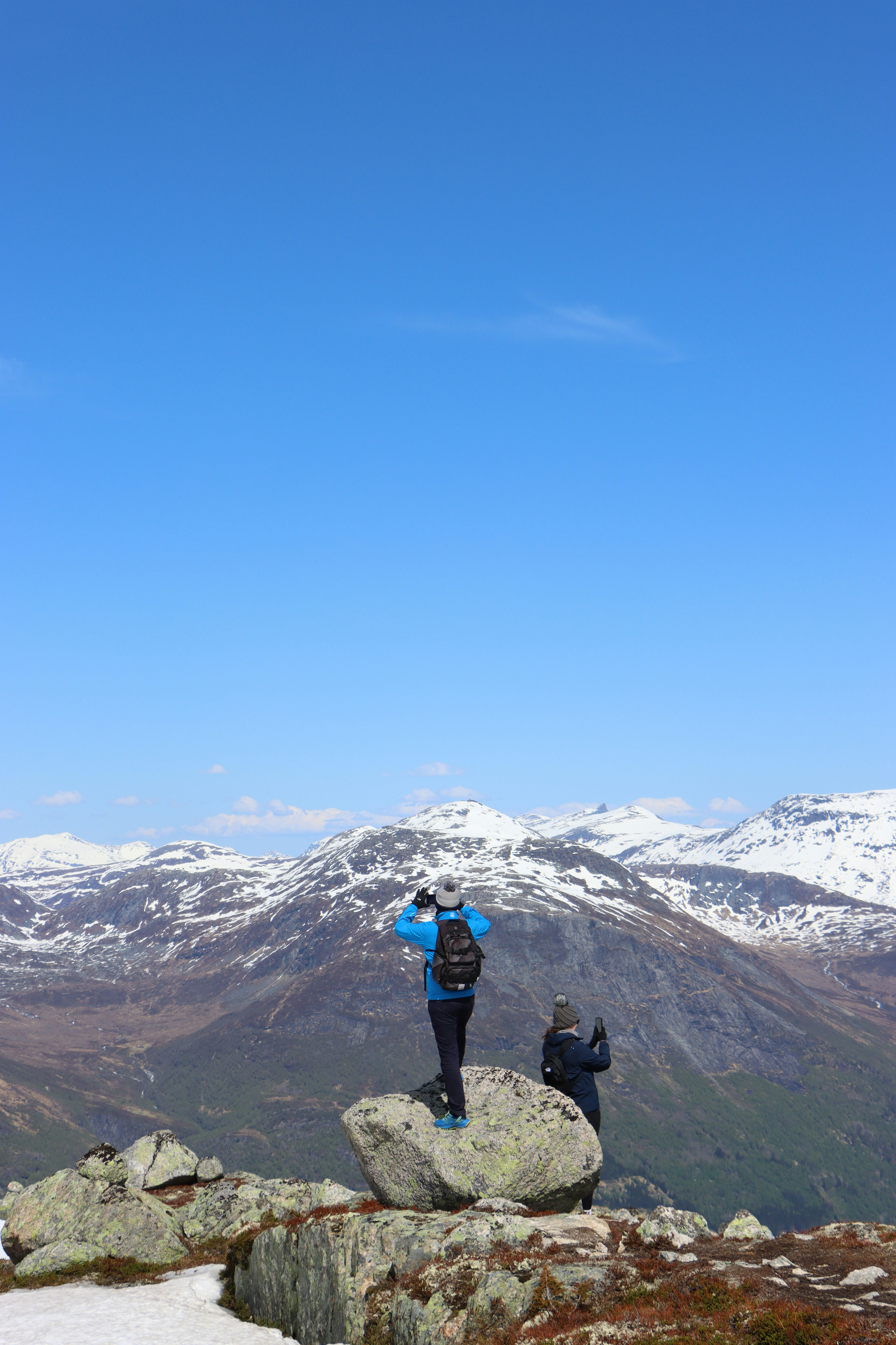 Two hikers on a windswept summit beneath a cobalt sky