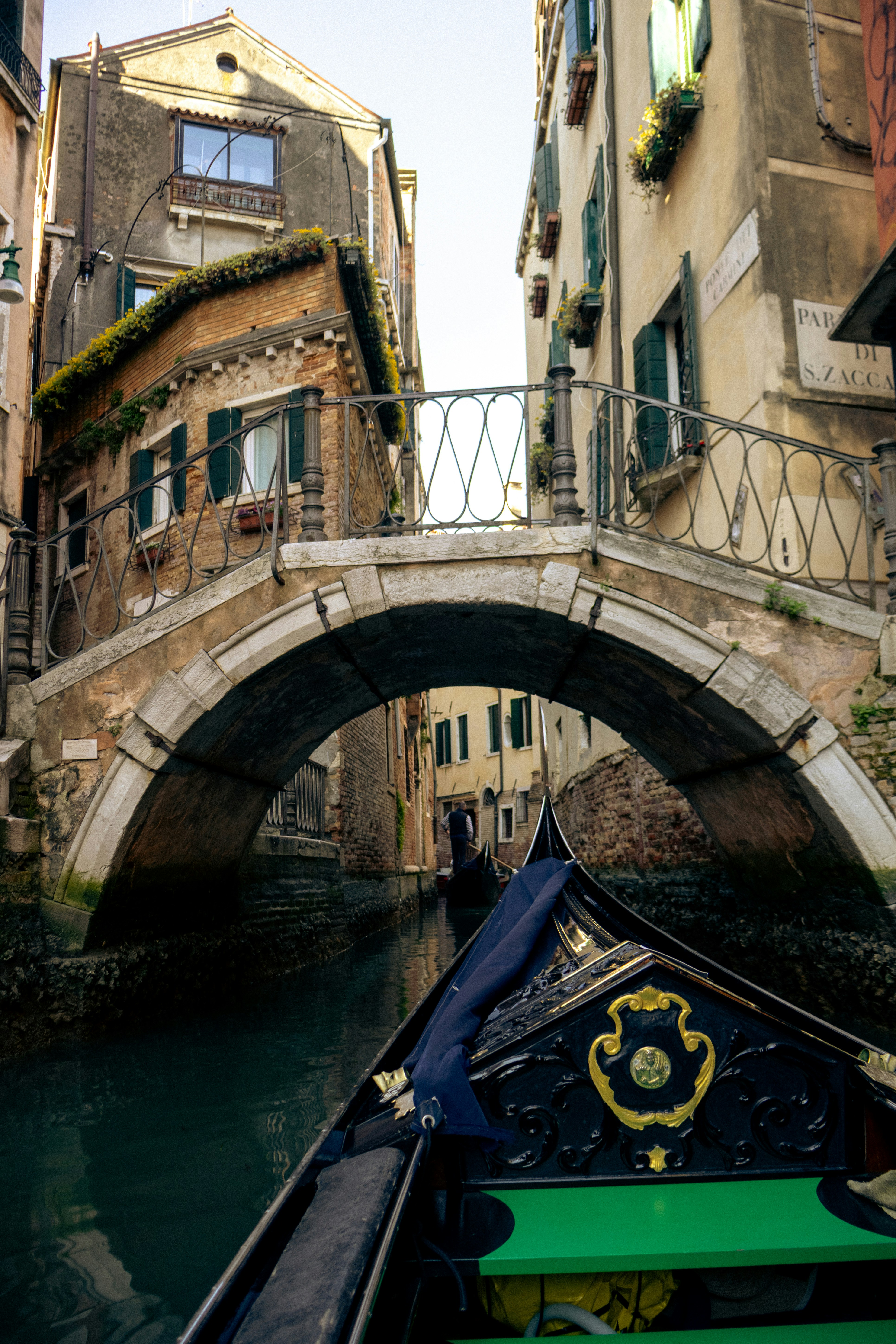 Gondola gliding beneath a weathered bridge in a sunlit Venetian canal