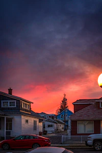 Sunset Over Quiet Suburb: A Red Car, Warm Sky, and Painted Houses
