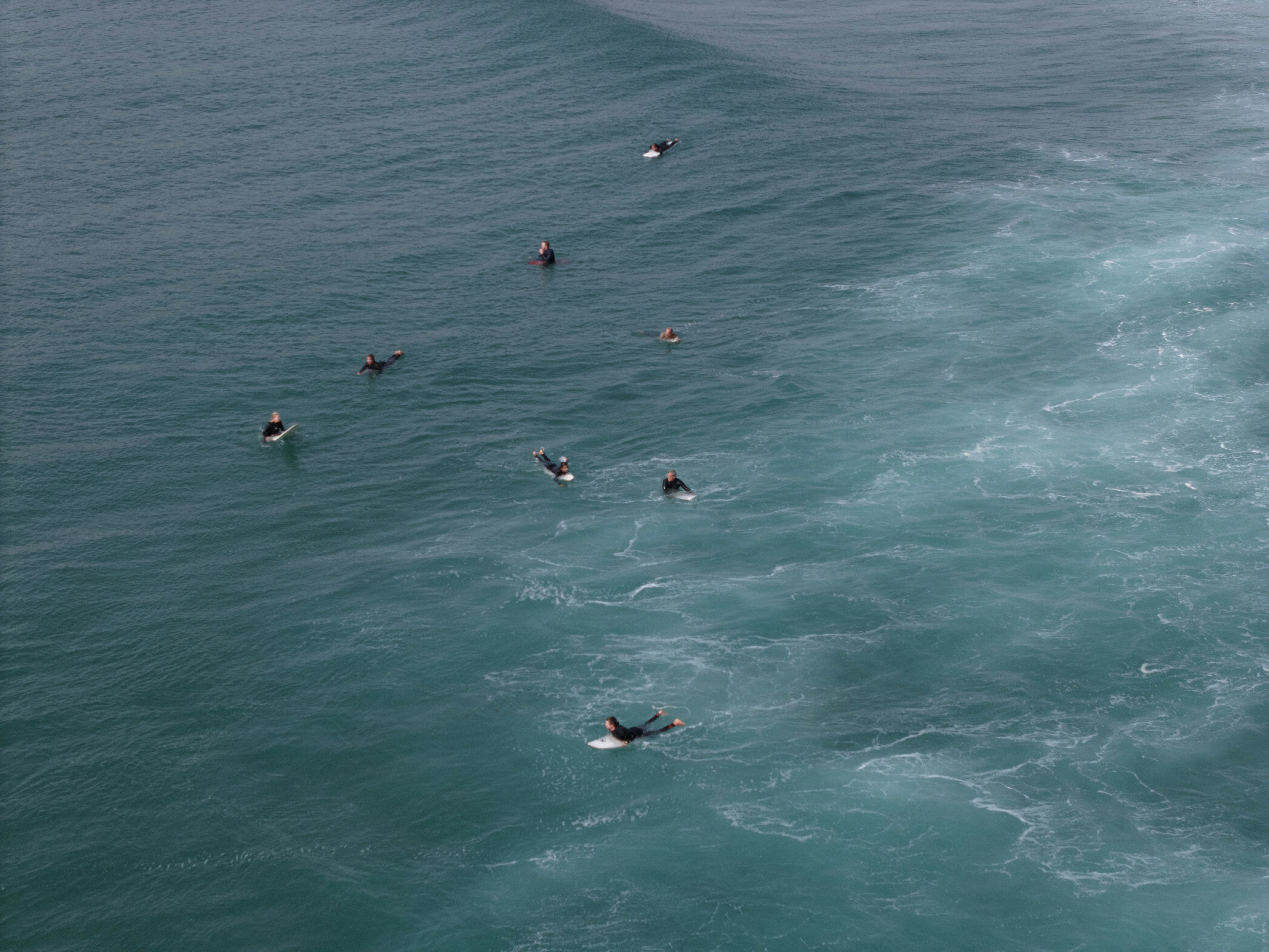 Synchronized dots: surfers tracing pale foam on a turquoise canvas
