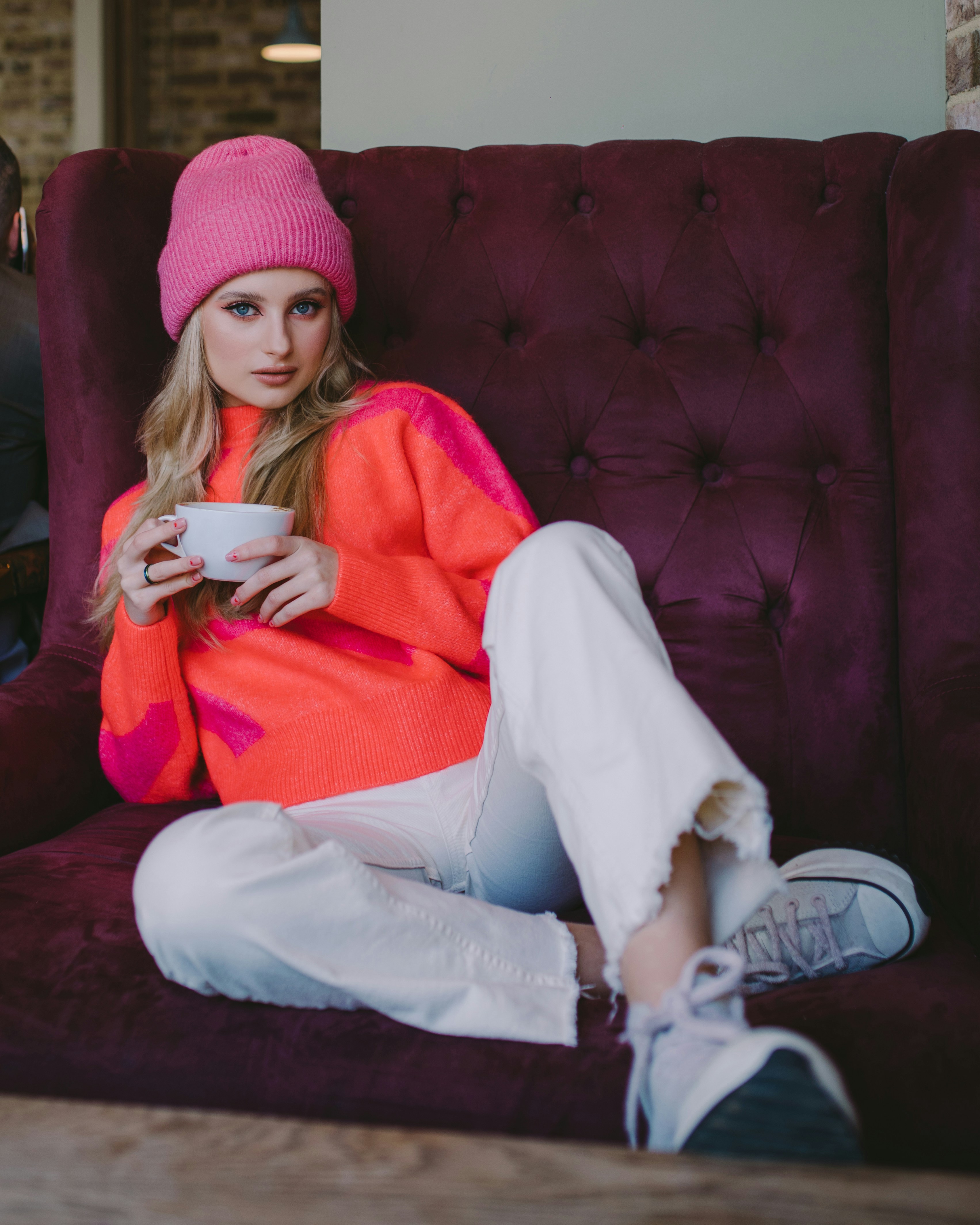 Cozy Neon Cozy: A Woman in a Pink Beanie Sips Quietly on a Velvet Couch