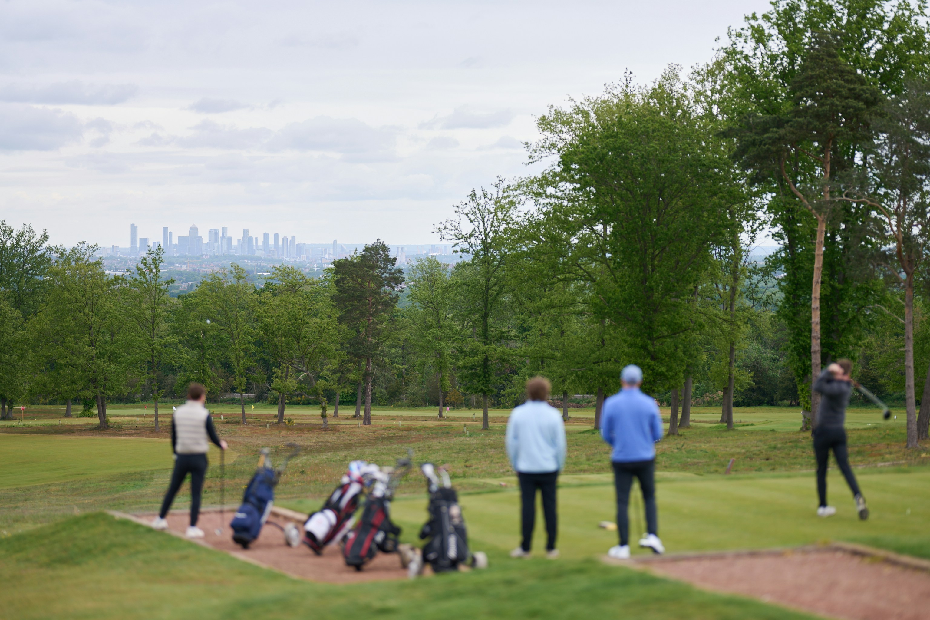 Golf Practice Scene: Players Align on the Tee with City Silhouette in the Distance