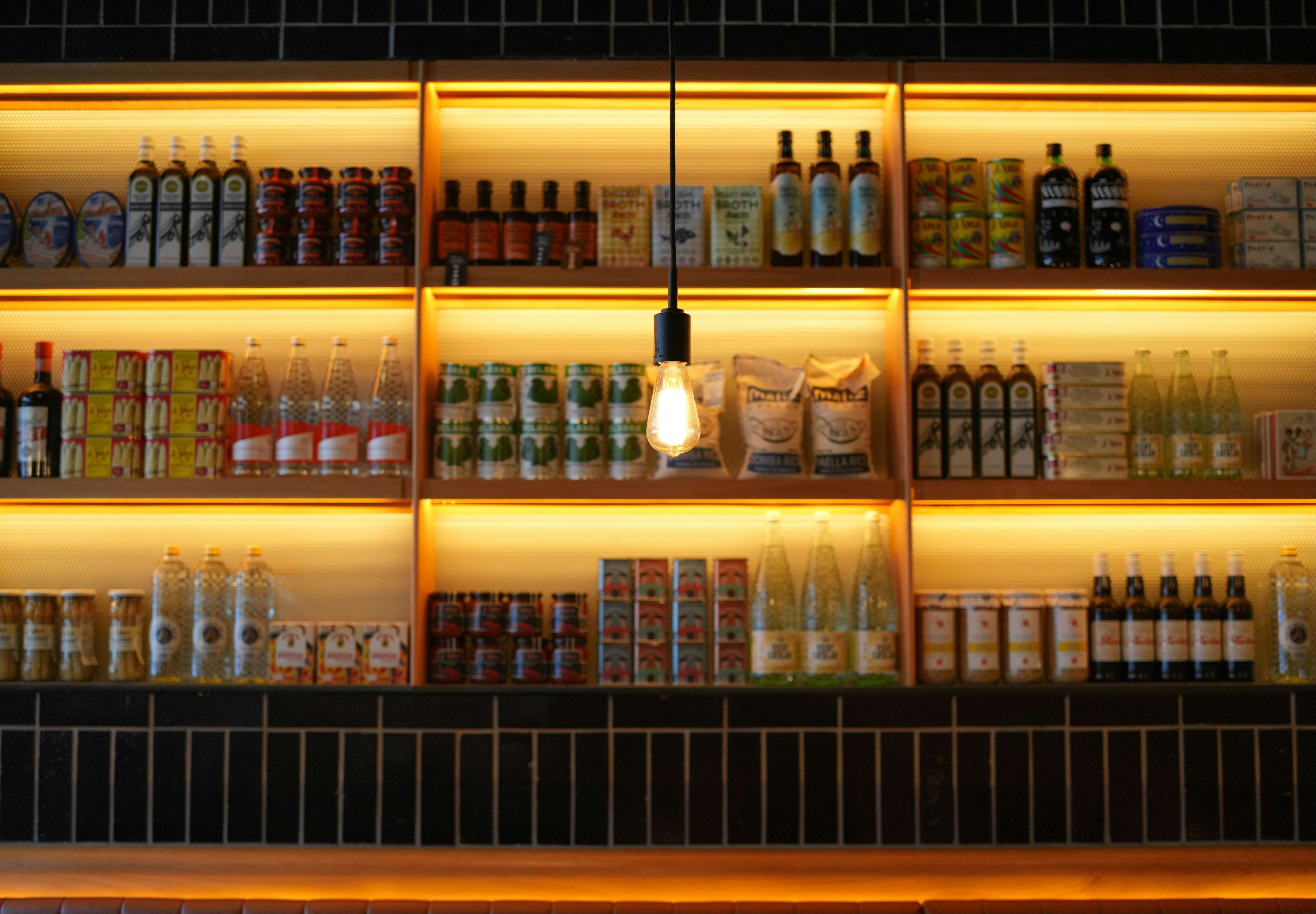 Horizon of Warm Bottles: Backlit Shelves Glow Through a Single Pendulum Bulb