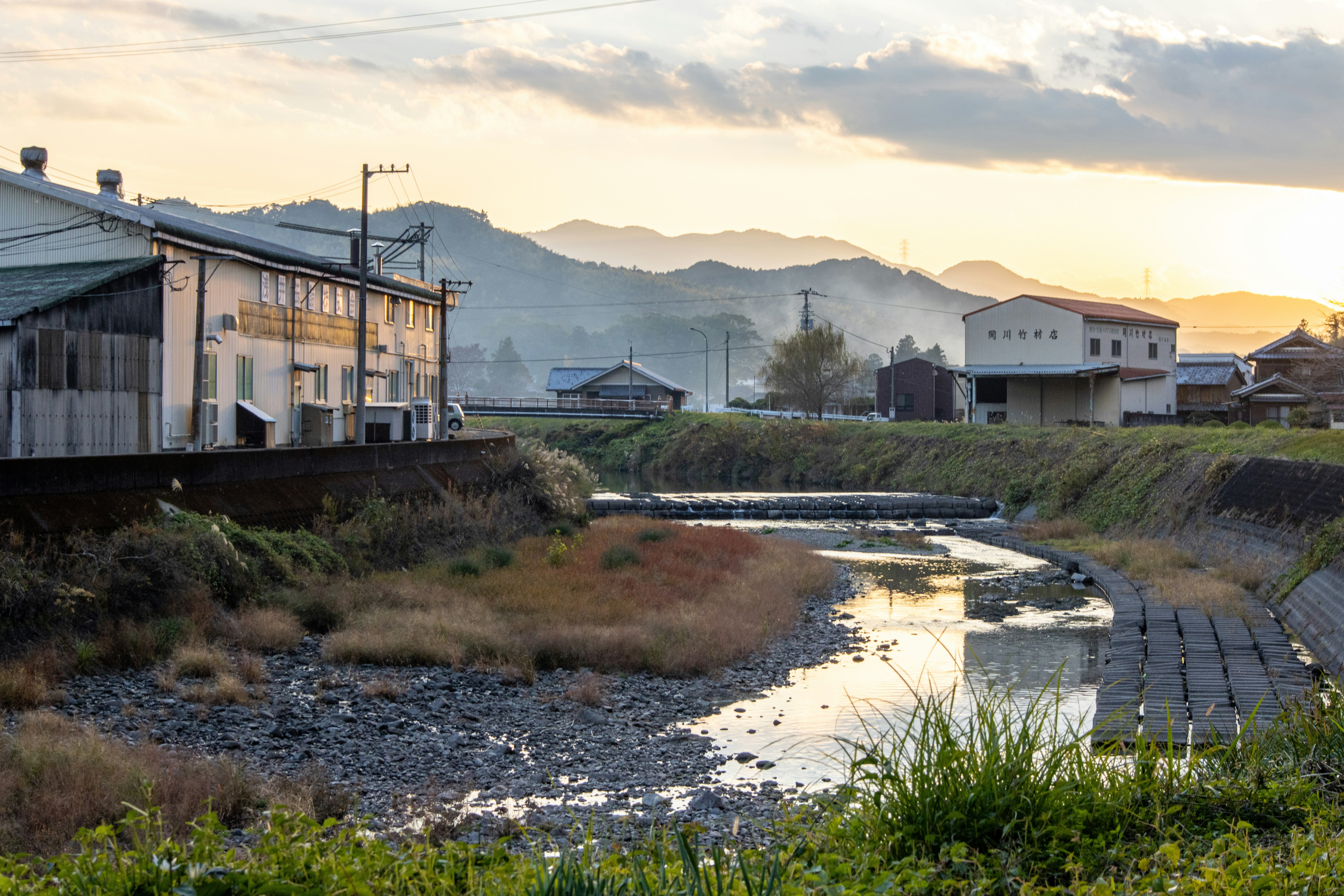 Sunlit Riverbank Between Quiet Buildings at Dusk