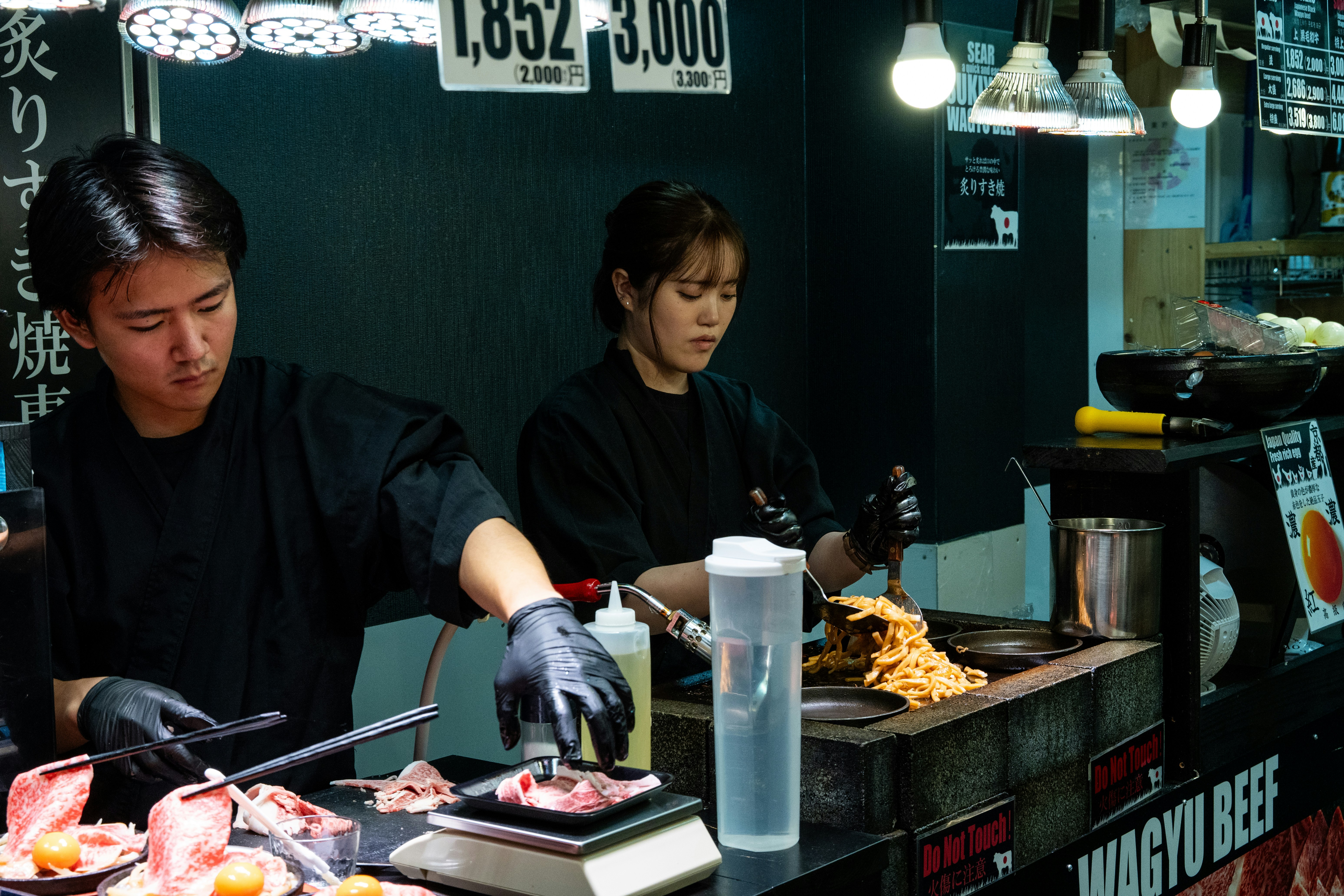 Chefs preparing meat and cooking dishes in a food stall.