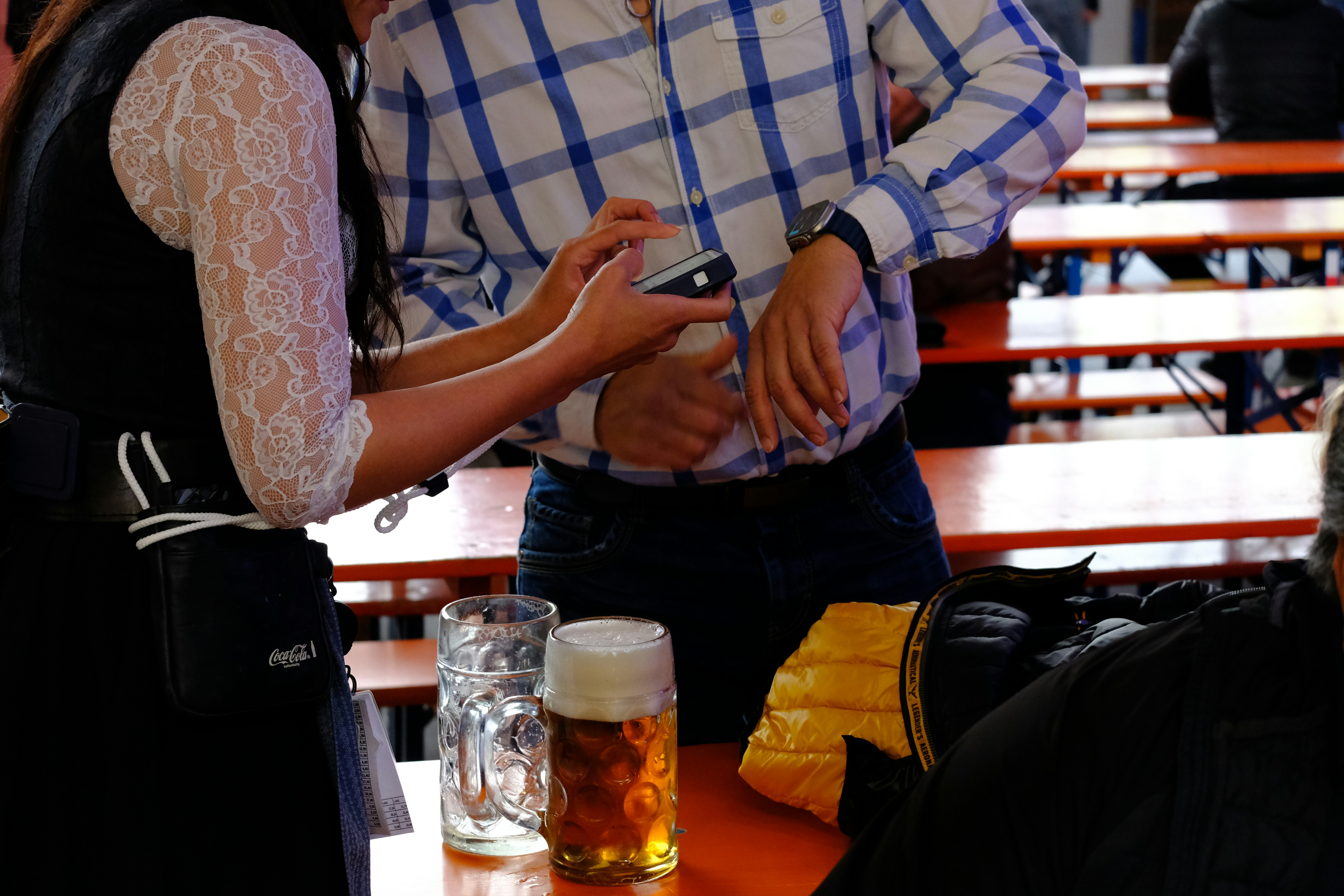 Conversations at the beer hall: two people sharing a phone behind a beer mug