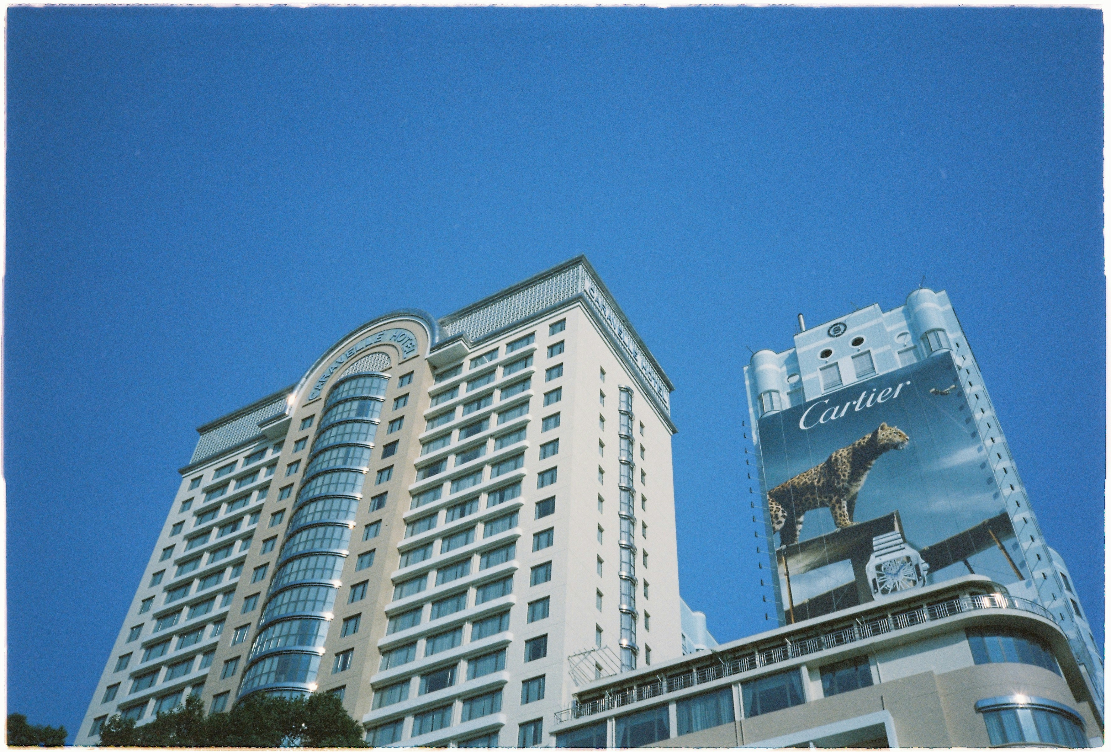 Two modern buildings with a cartier advertisement under blue sky.