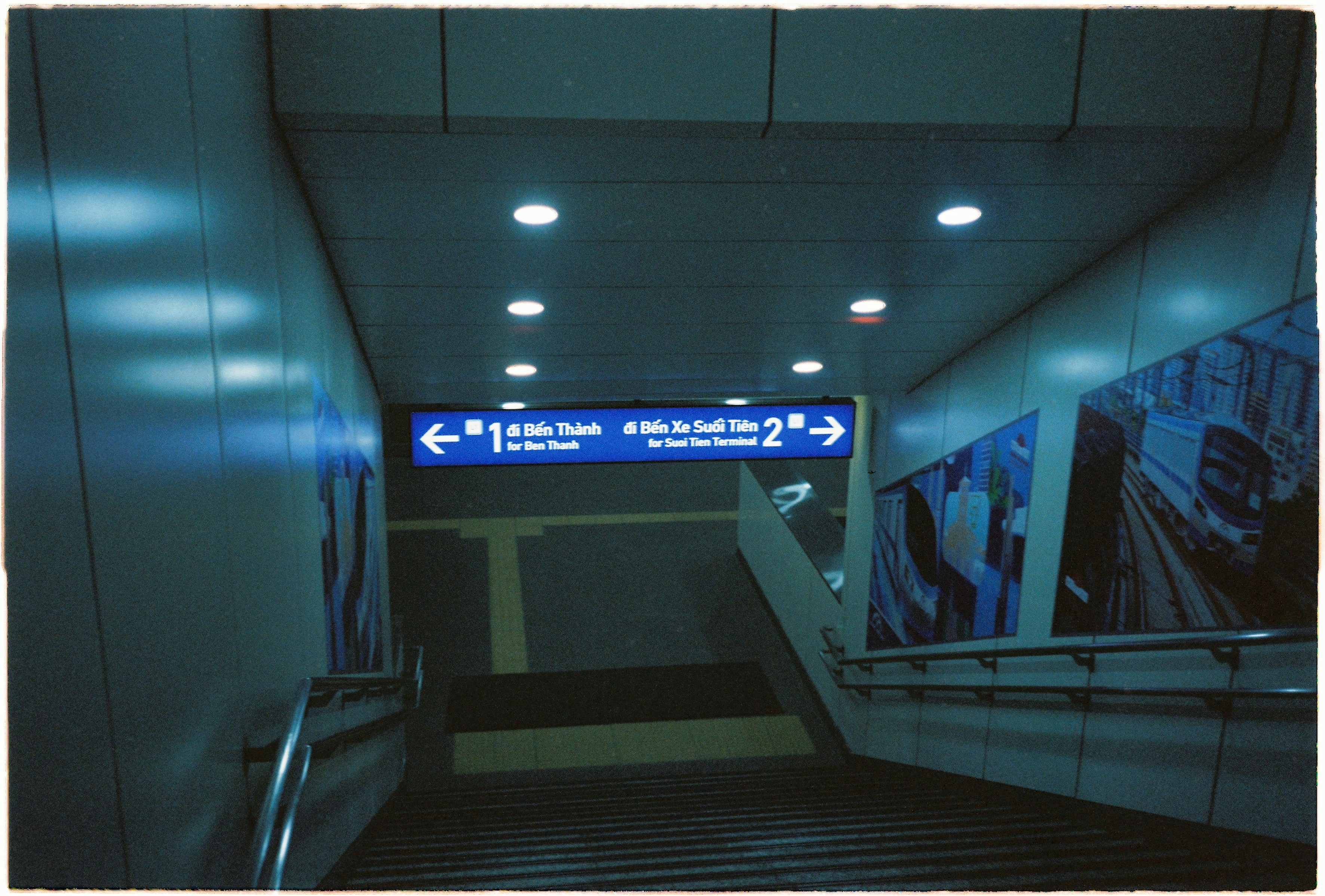 Dimly lit subway staircase with a blue directional sign.