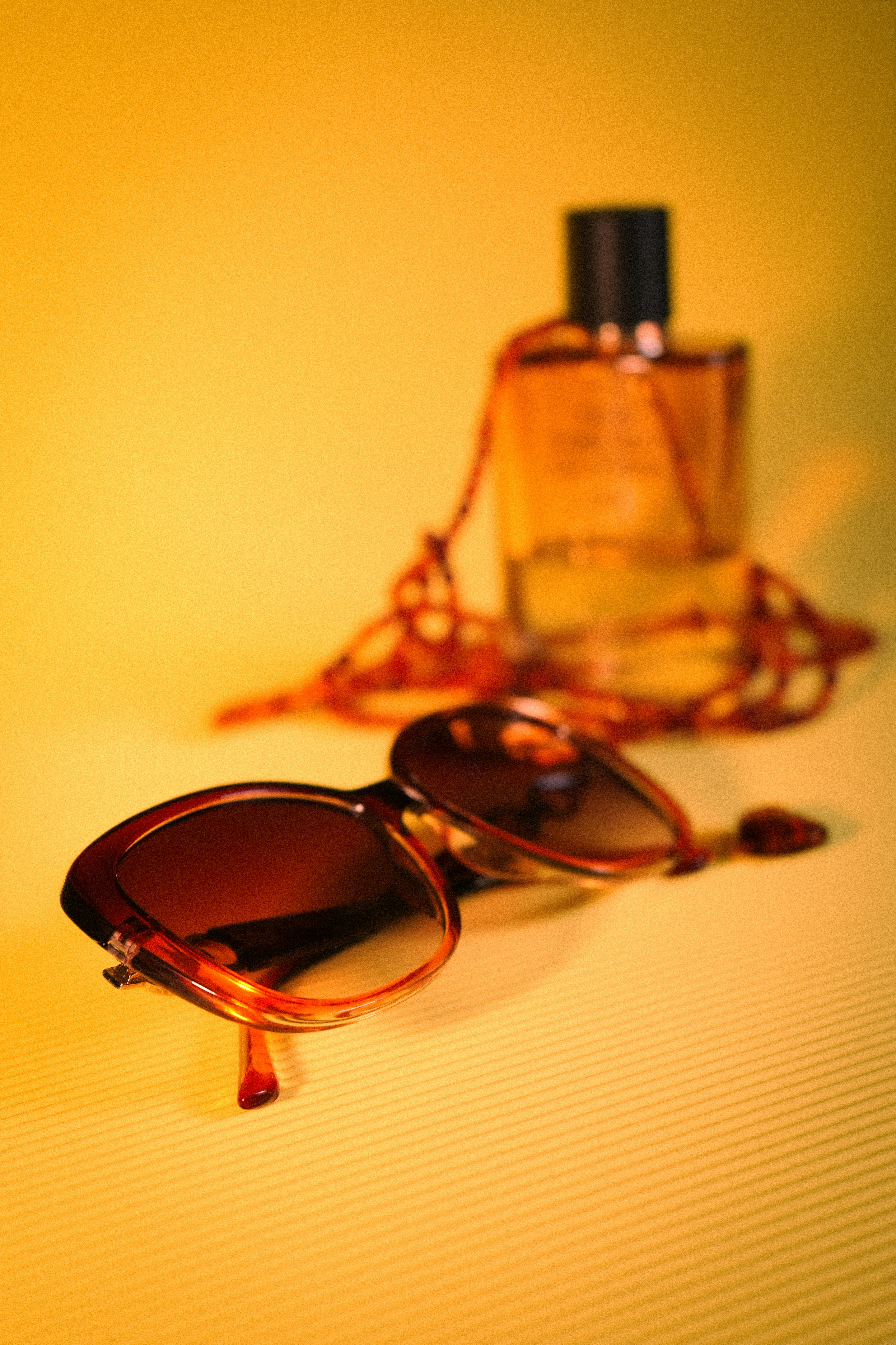 Amber Echoes: A Close-Cropped Still of Sunglasses and Perfume on Warm Yellow