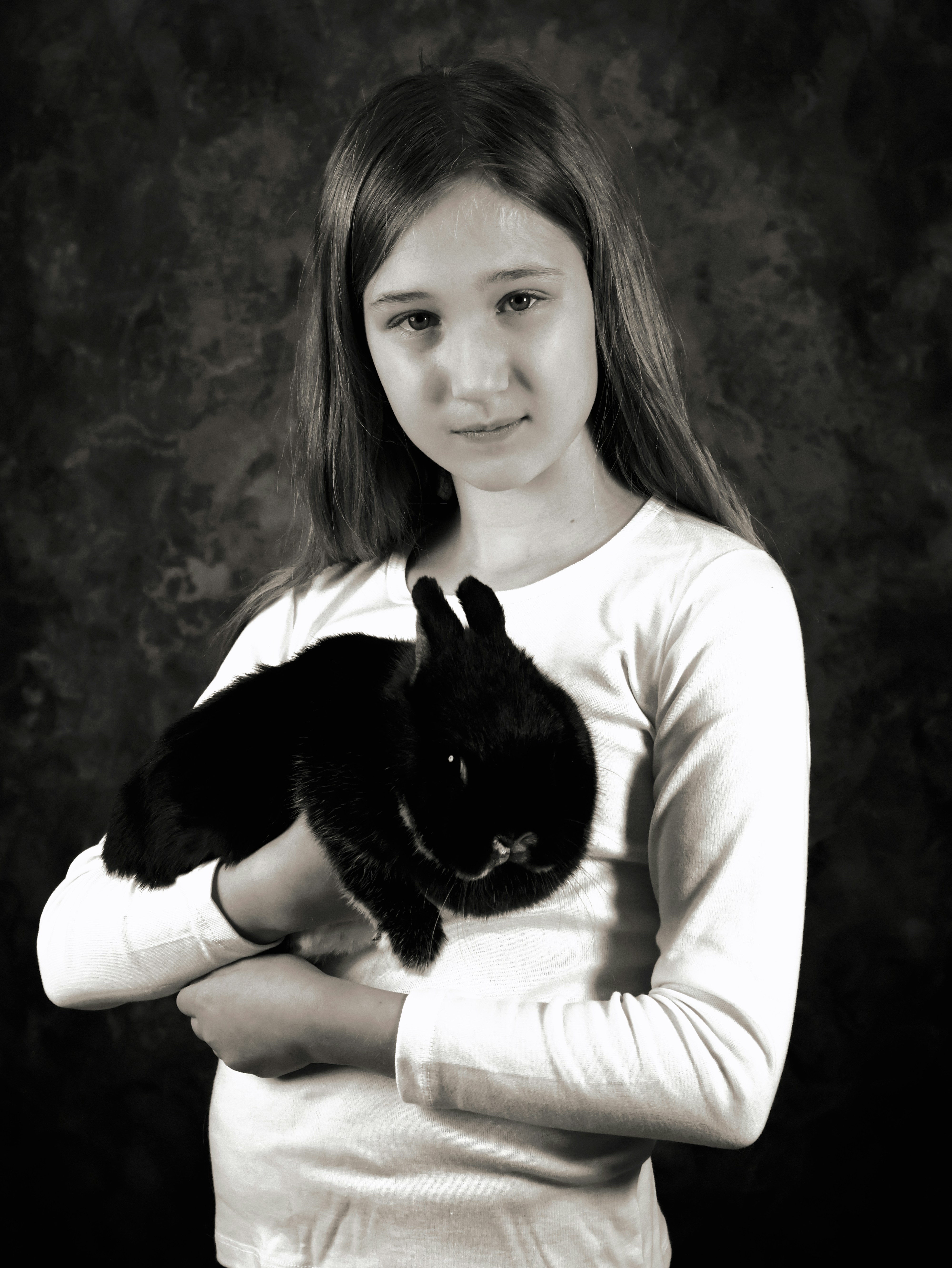 Girl in White Holds Black Rabbit Against a Textured Backdrop