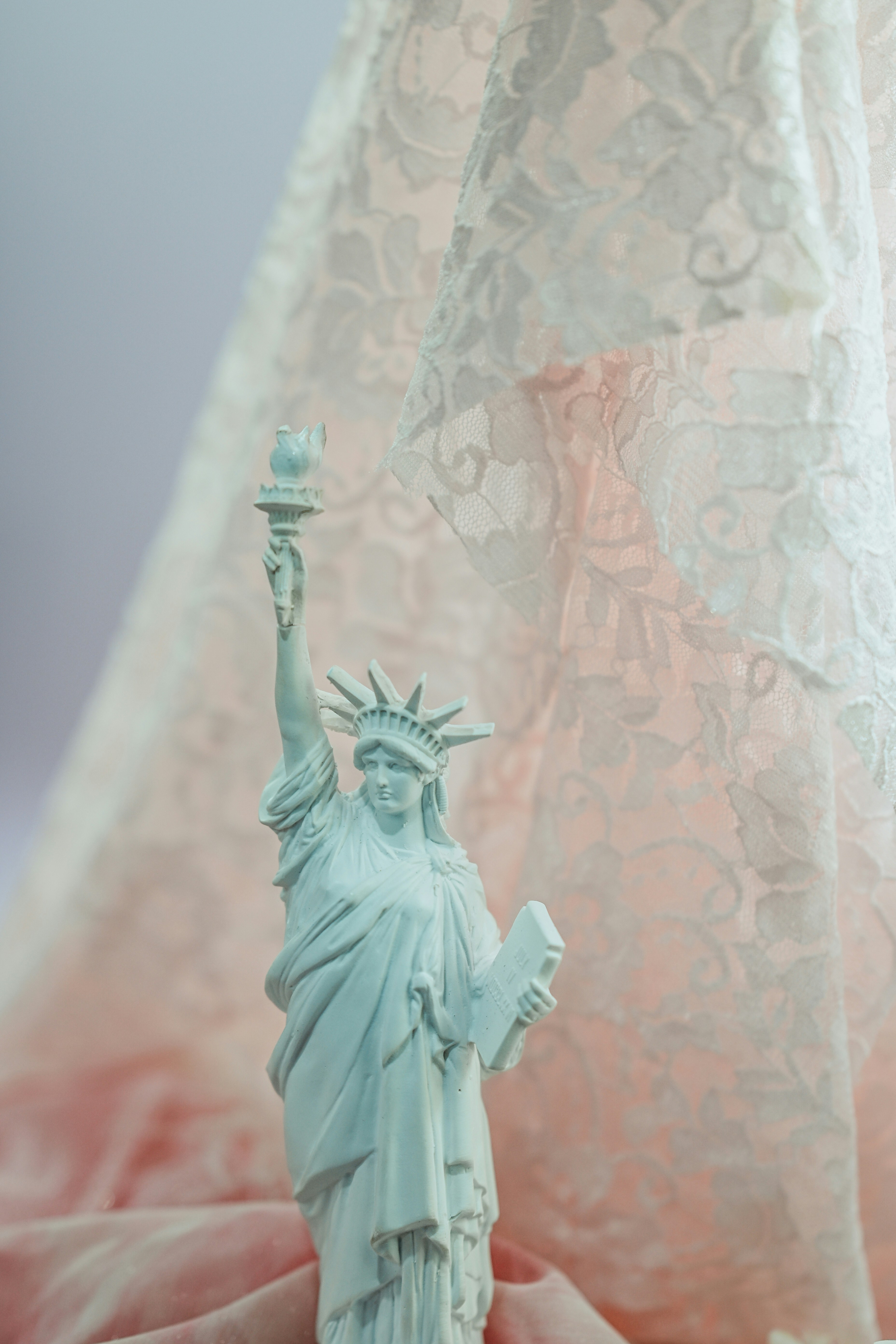 Statue of Liberty miniaturized: mint-toned replica against lace backdrop