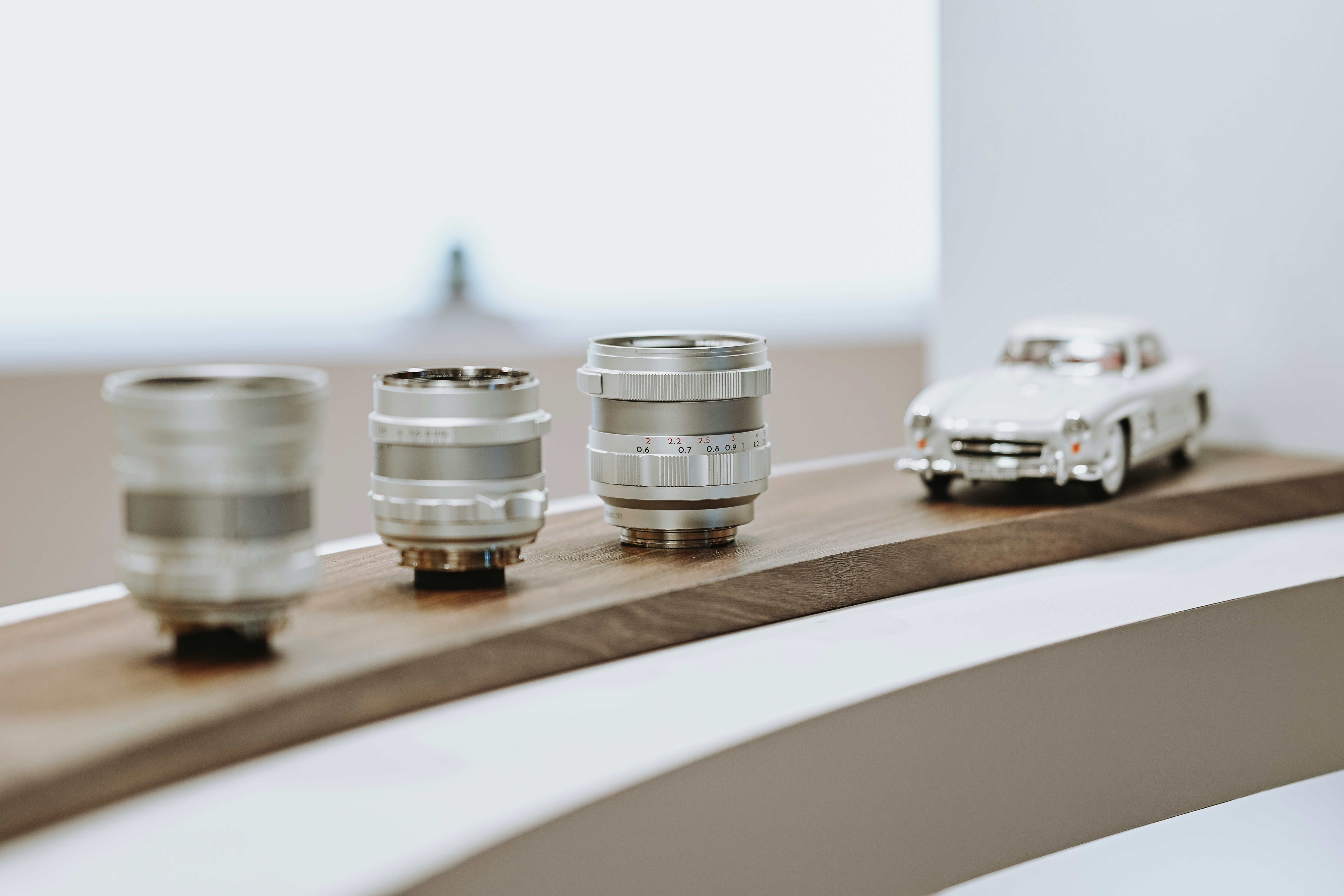 Miniature Lens Parade: A Row of Silver Cylinders and a Tiny Car on a Wooden Curve