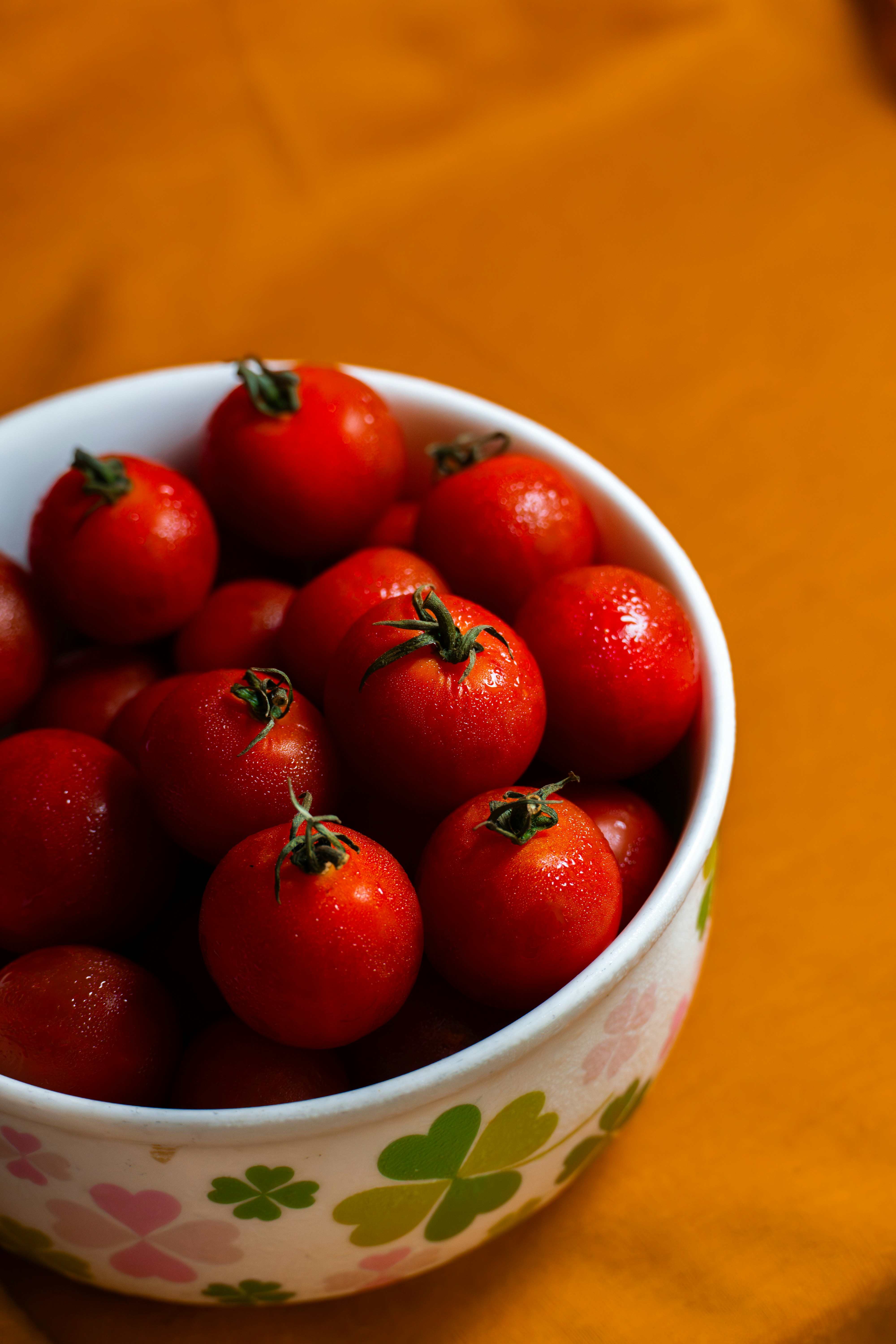 Crimson Bounty: A Bowl of Cherry Tomatoes on a Sunny Orange Cloth