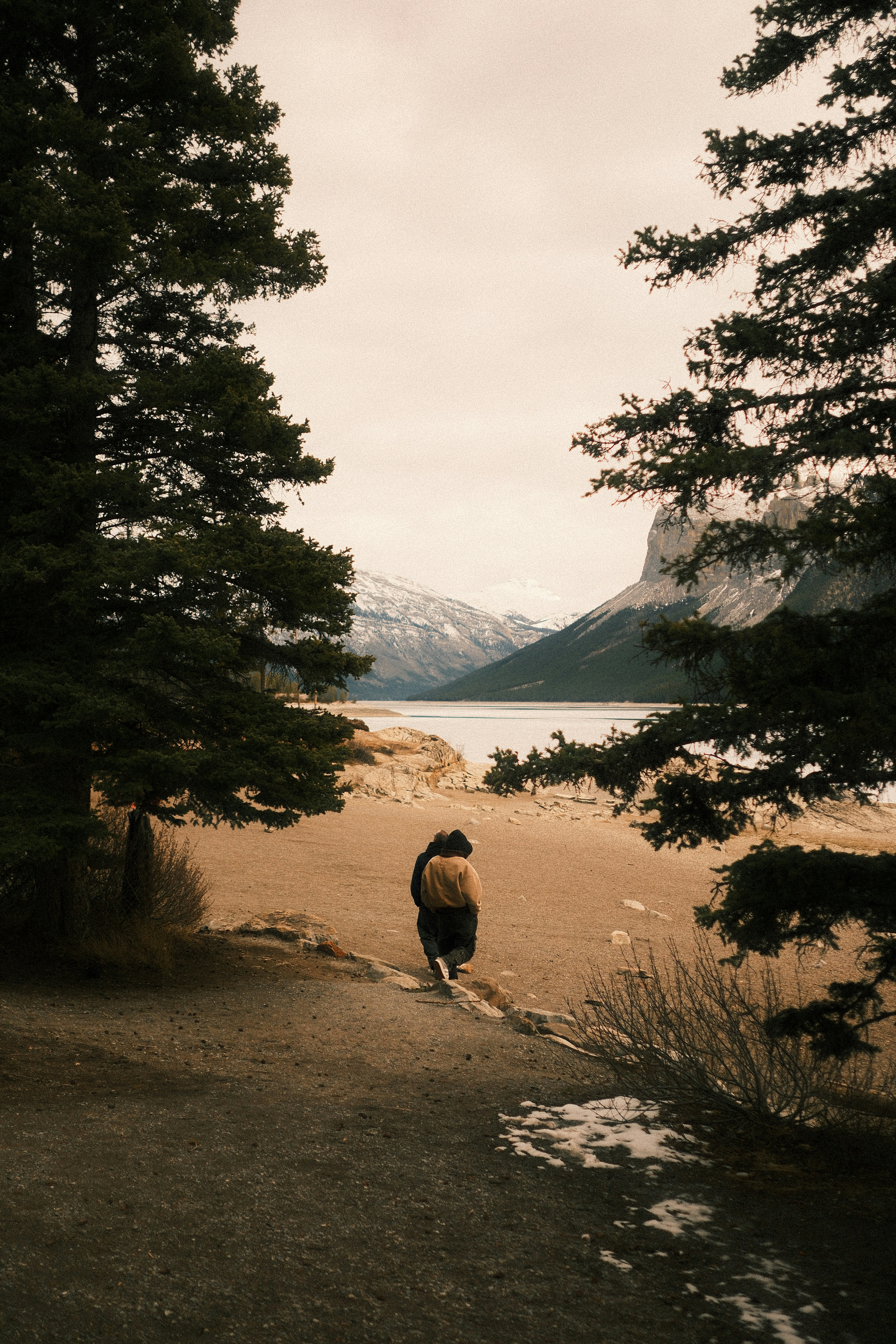 Two Wanderers at the Edge of the Lake Between Pines and Peaks