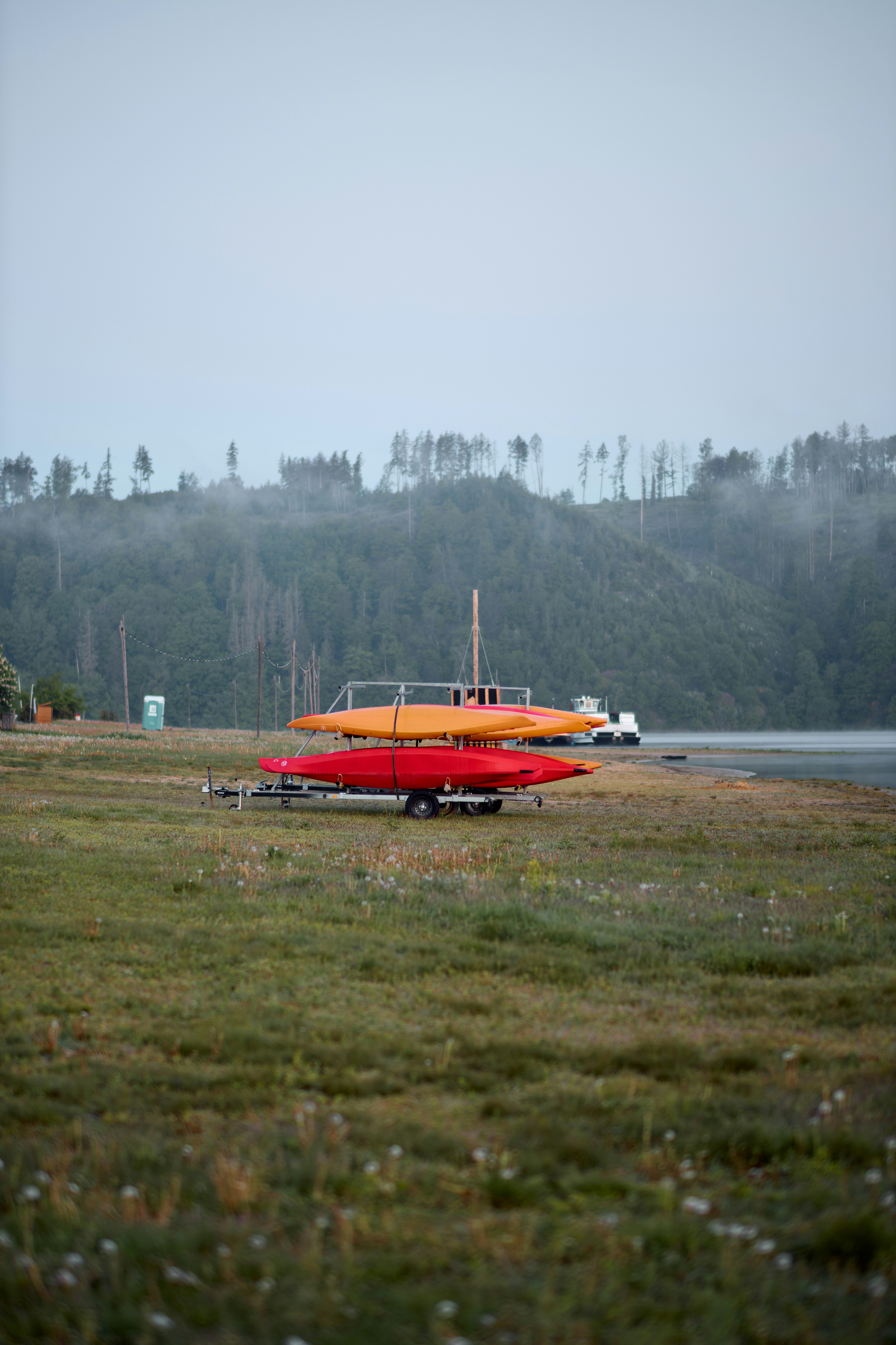 Red and yellow boats on grass near a foggy forest.