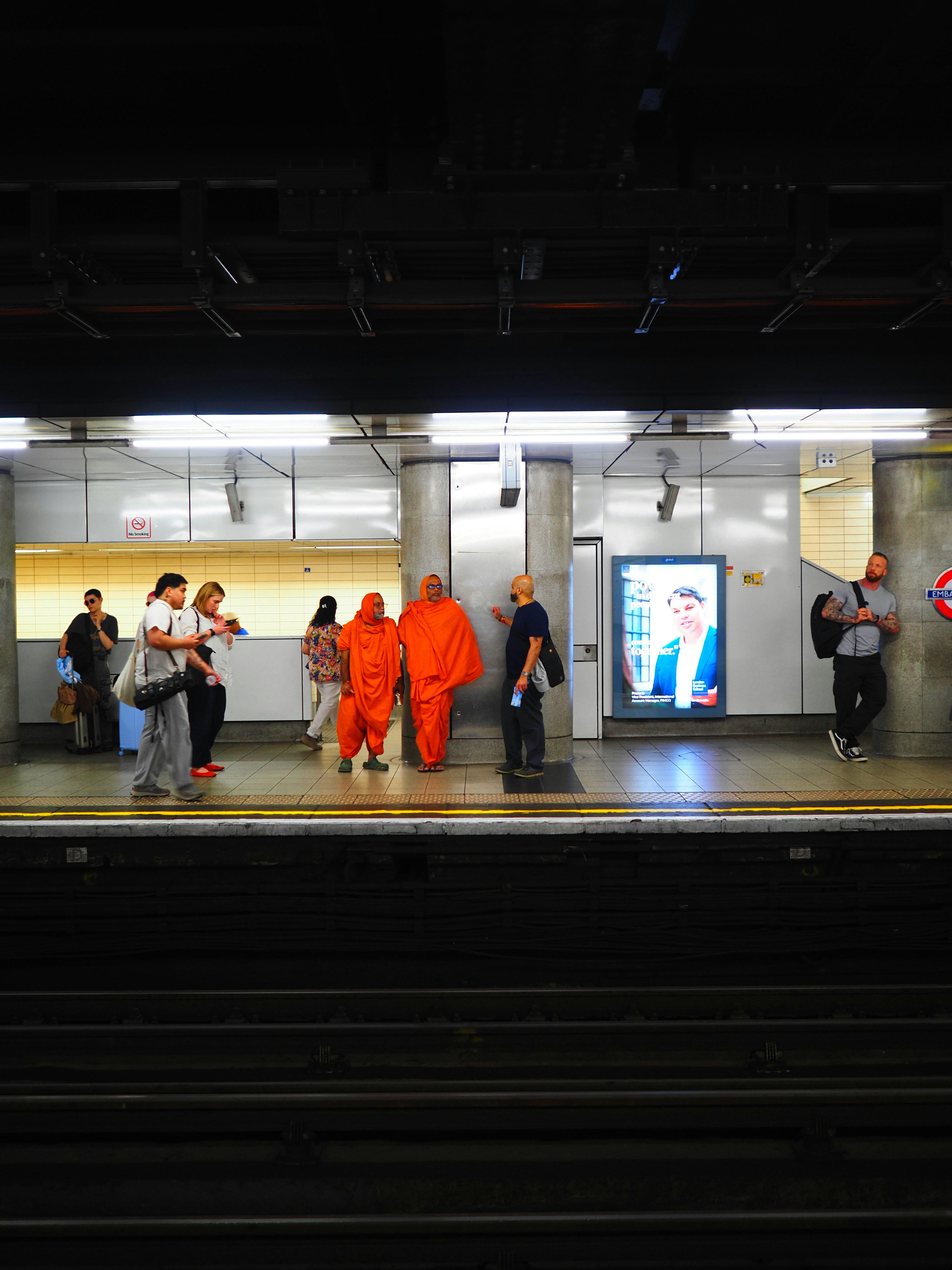 underground scene where vibrant orange robes cut through the muted tones of a London Underground platform, creating a cinematic contrast between movement, culture, and city life.